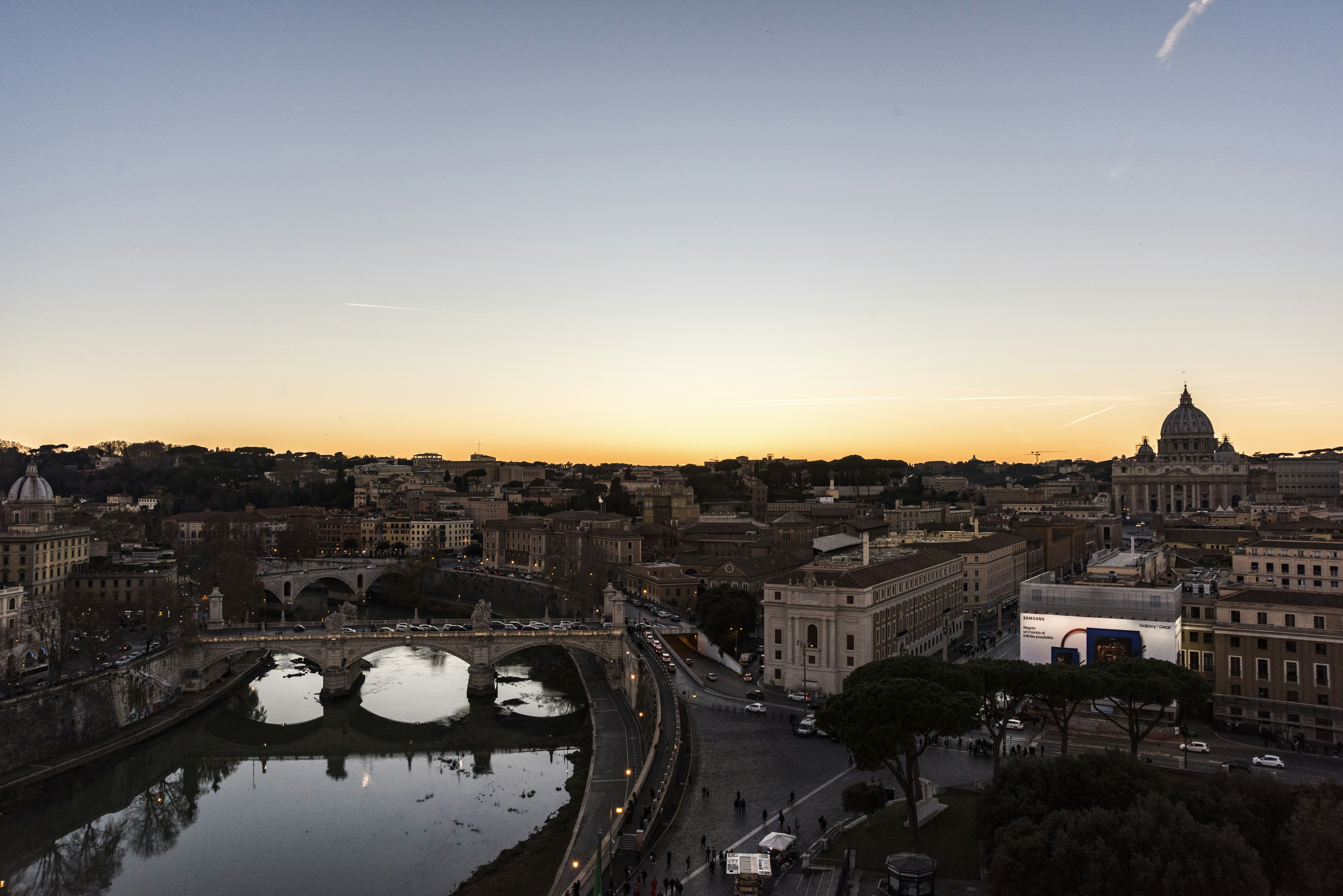 Golden sunset over Rome with the Tiber River reflecting city lights and silhouetted architecture.