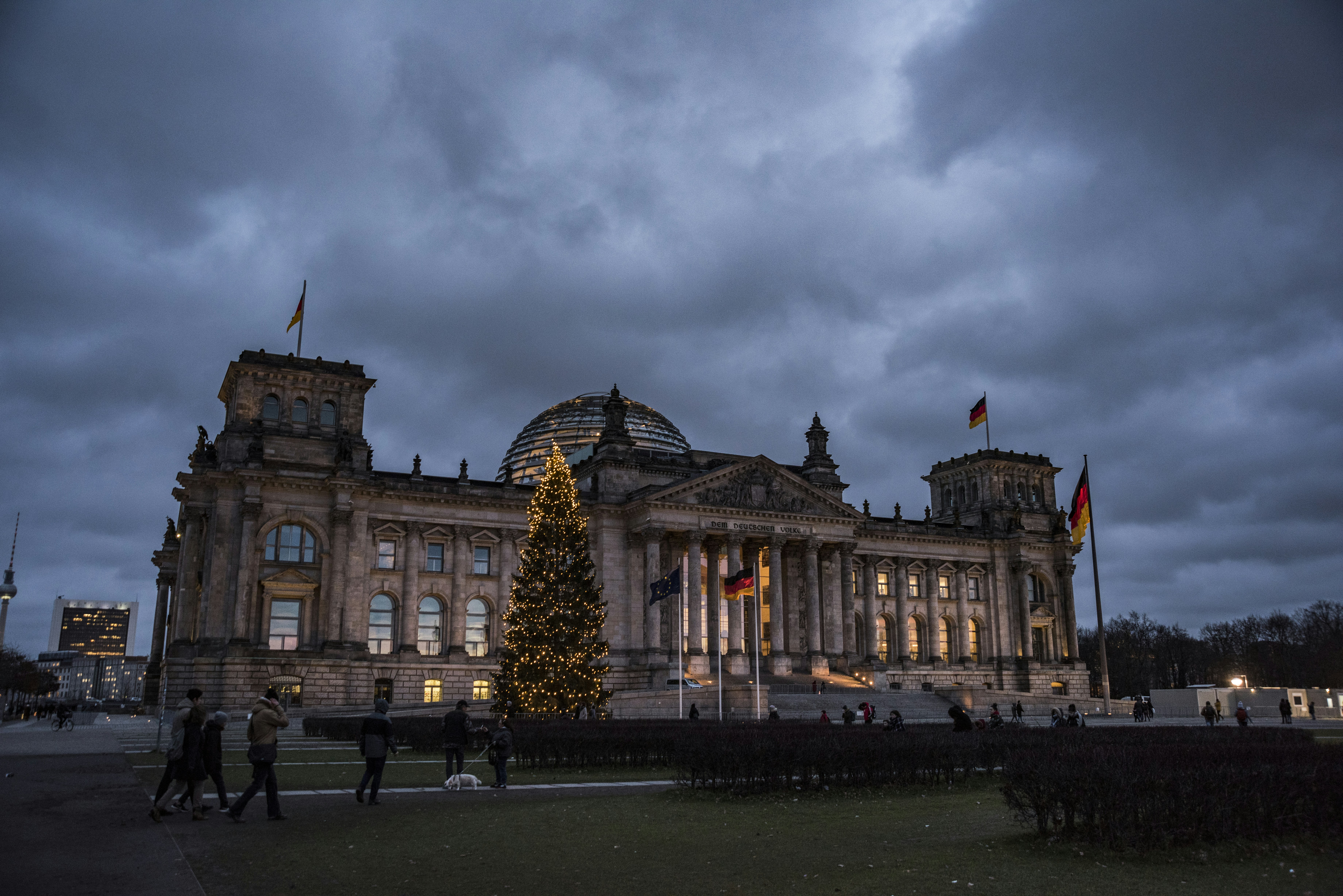 Reichstag building adorned with a glowing Christmas tree under a moody evening sky.