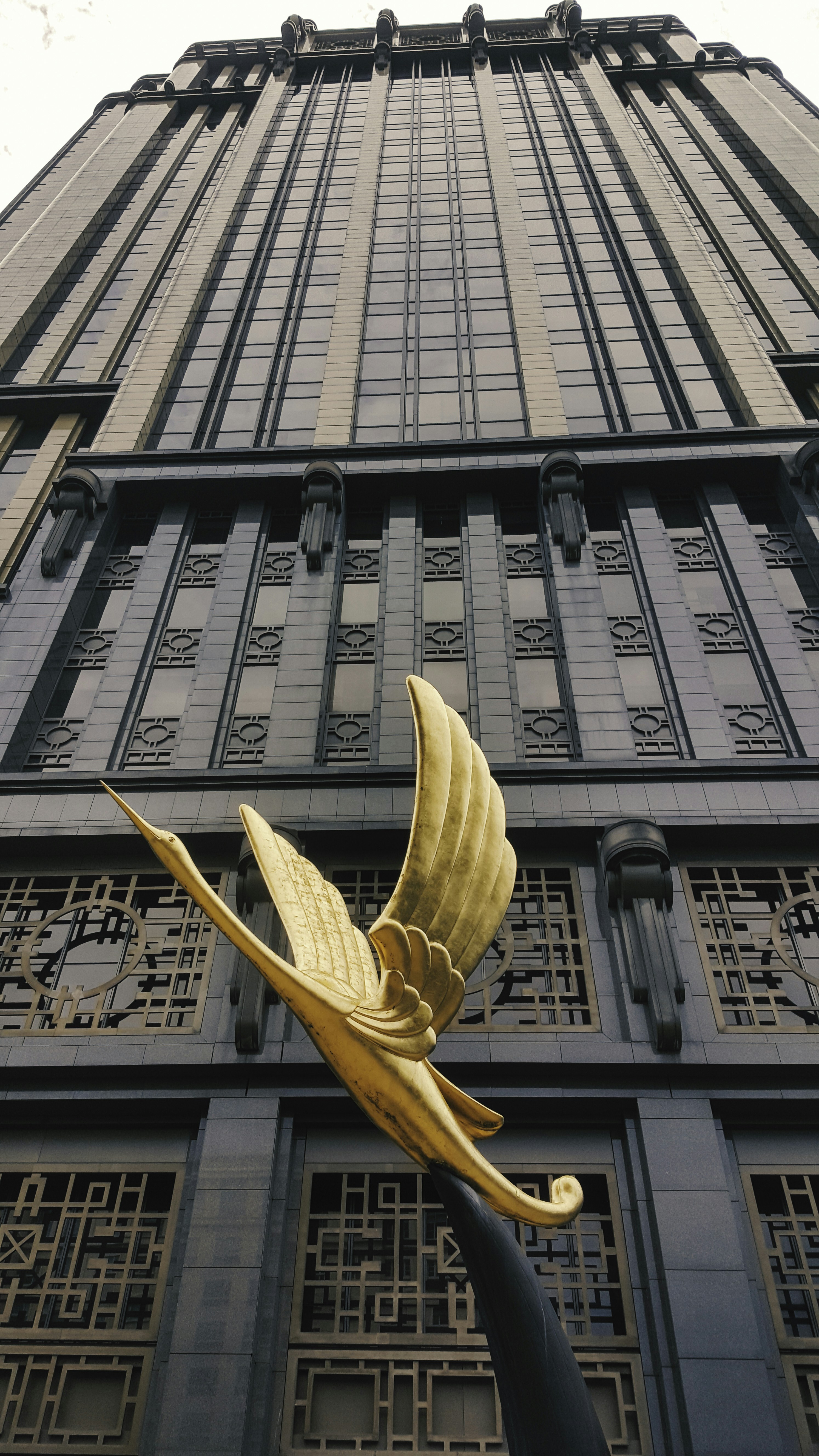 Low-angle shot of a gilded bird sculpture in the foreground, set before a tall, ornamental Art Deco facade.
