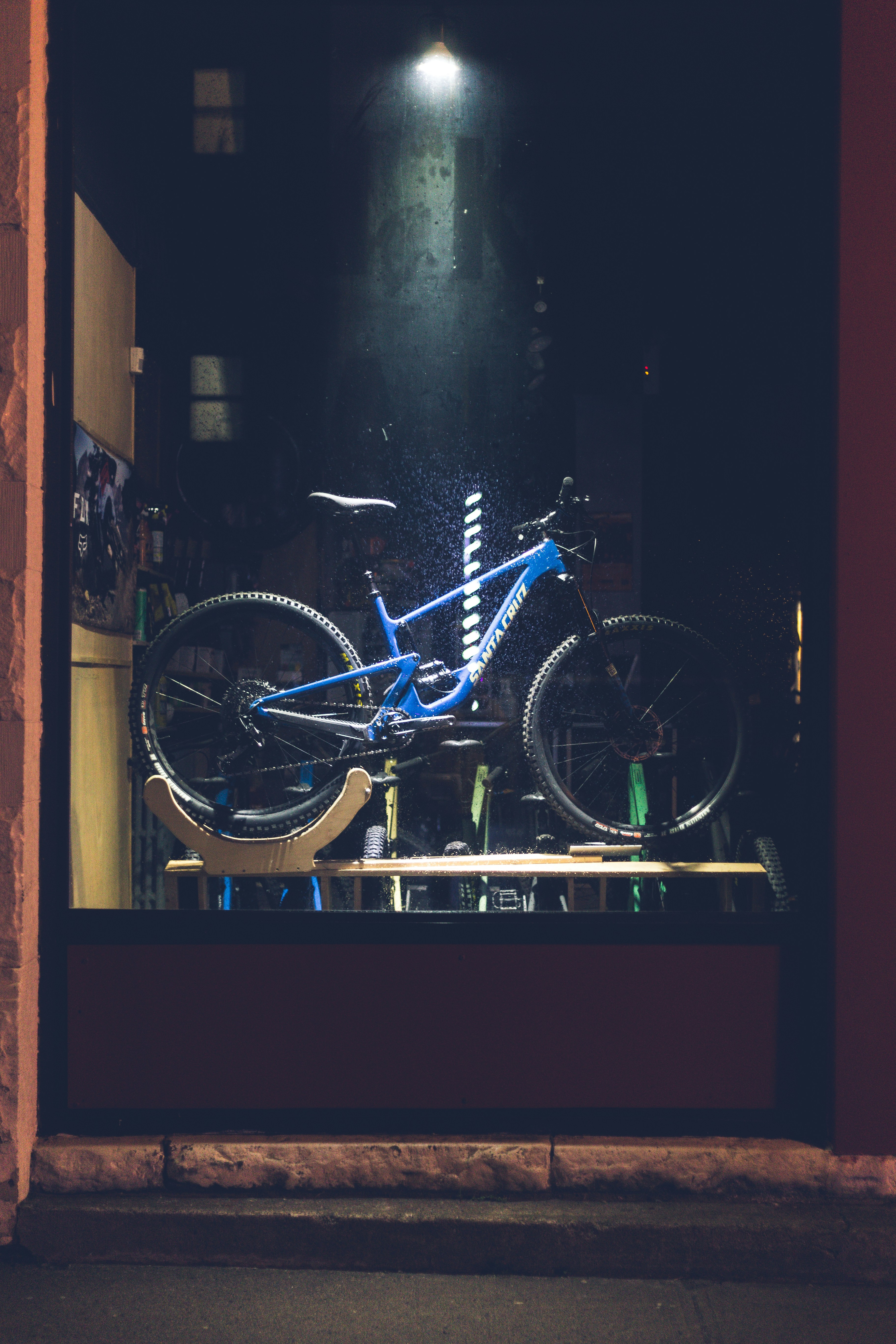 A blue mountain bike prominently displayed in a shop window, illuminated by soft lighting amidst a dark urban backdrop.