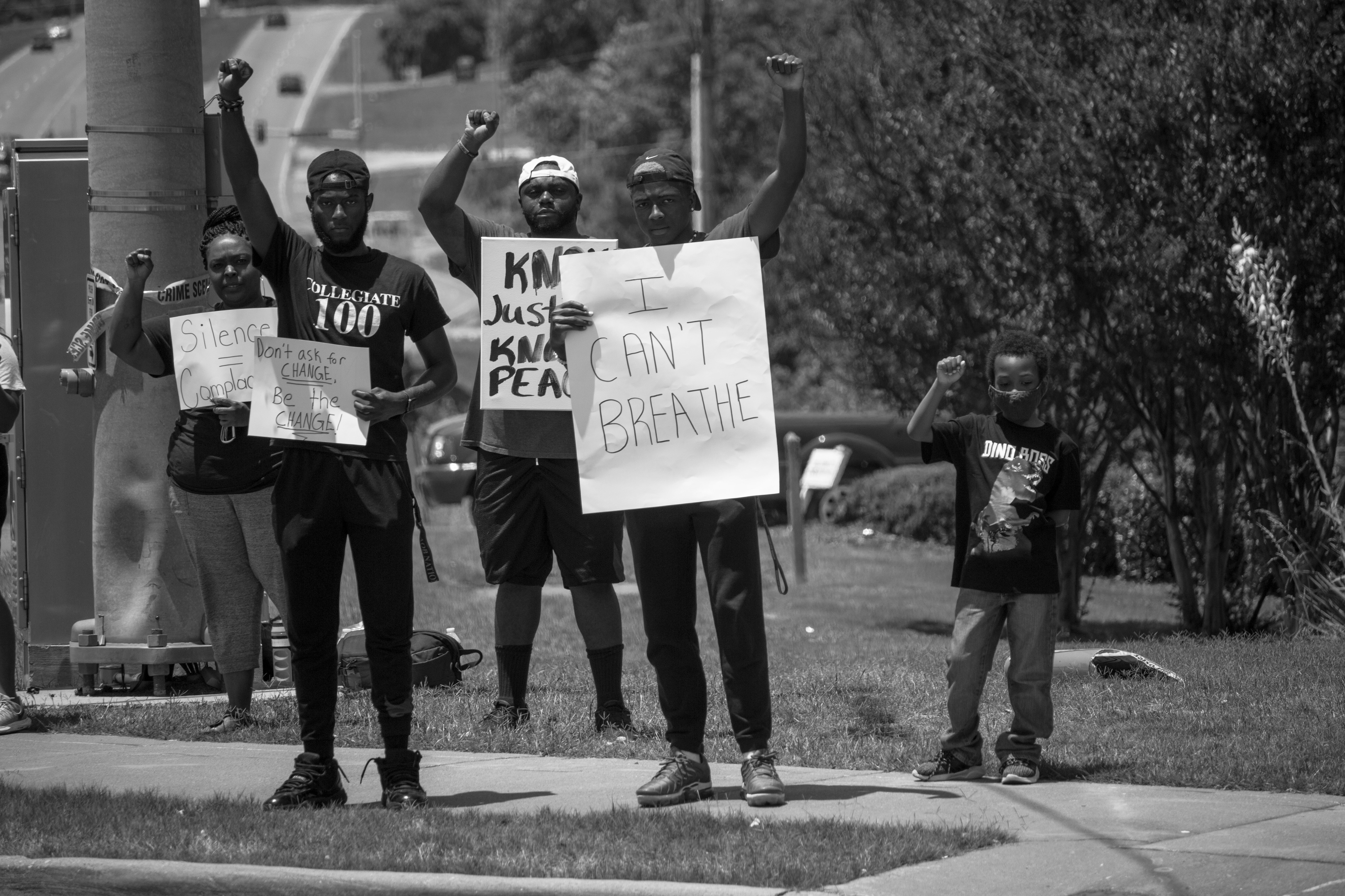 Group holding signs and raising fists at a roadside gathering.