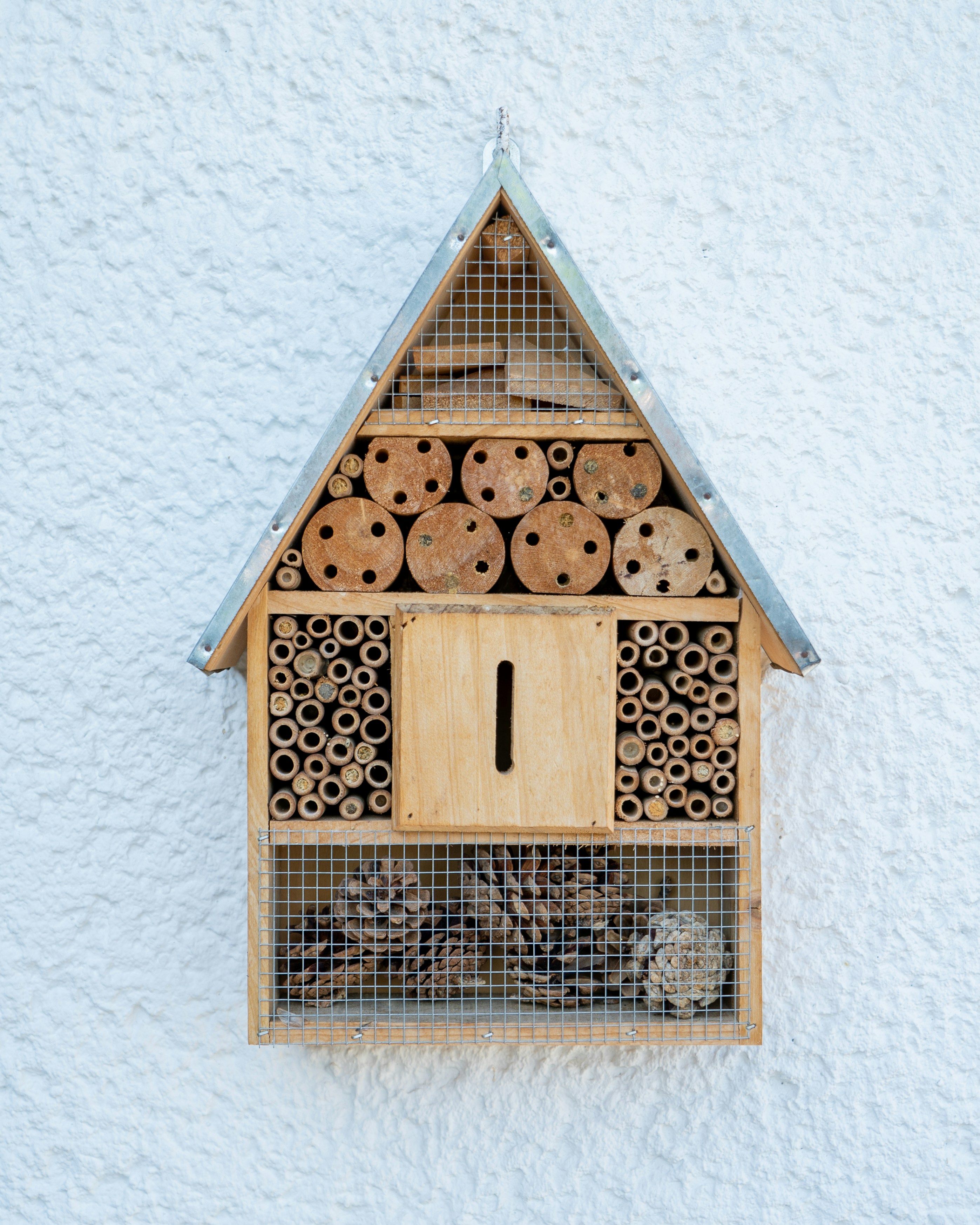 Wooden insect hotel designed for pollinators, featuring various natural materials and compartments for nesting. Ideal for supporting local biodiversity.