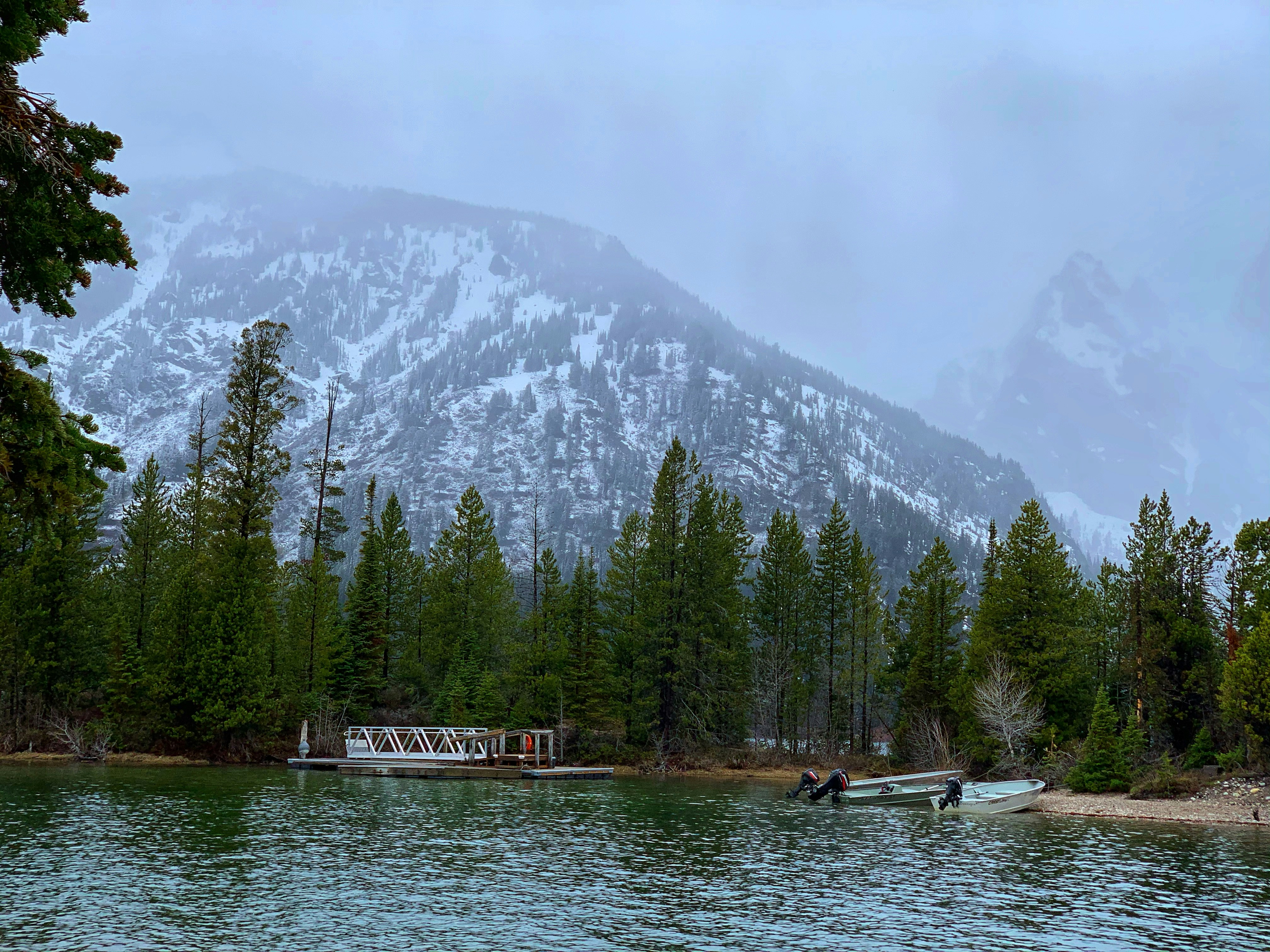 A serene alpine lake framed by snow-capped mountains and lush evergreens, featuring a boat and a dock nestled along the shoreline.