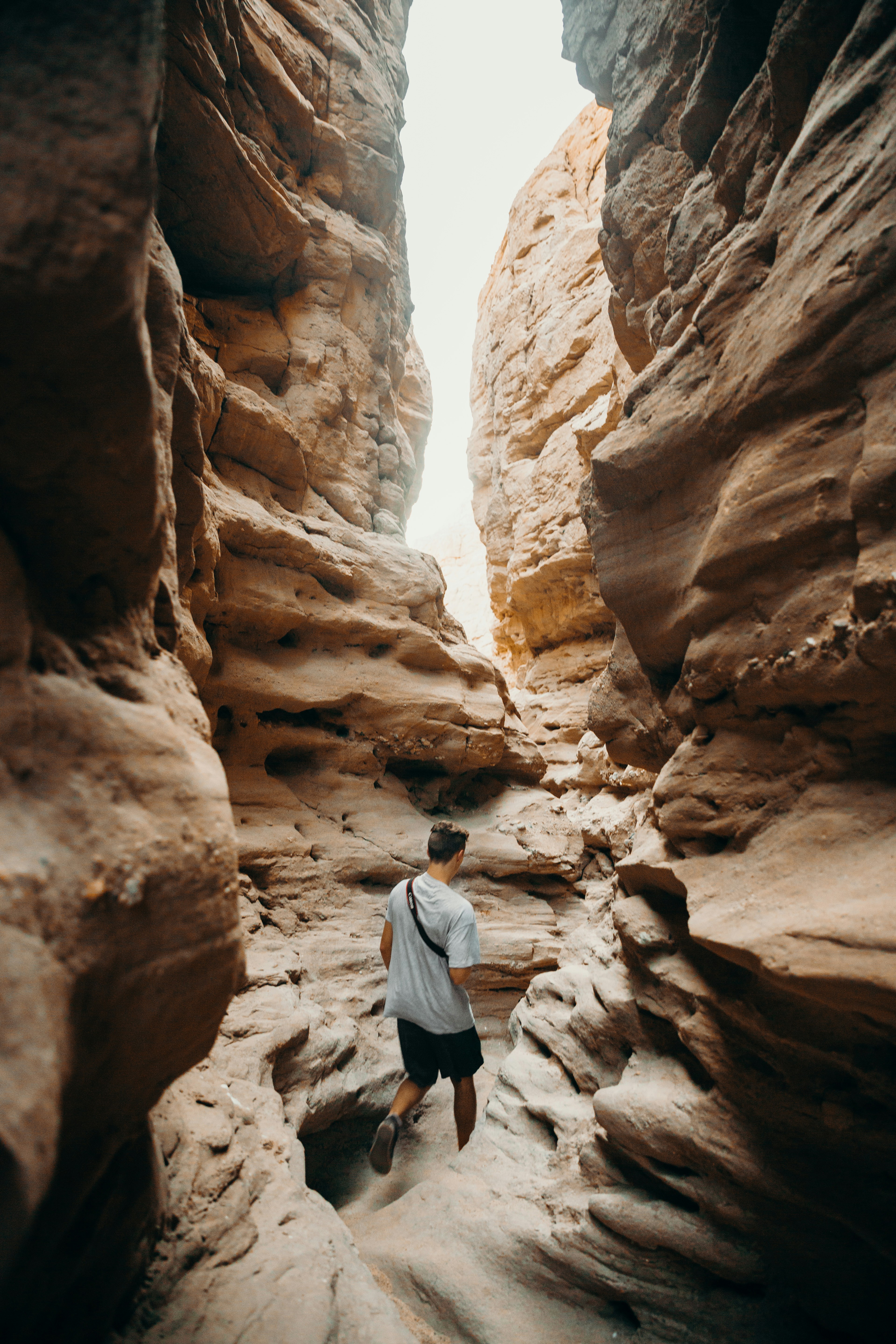 A solitary figure navigates a narrow canyon, surrounded by intricately carved rock formations. The soft light filtering through the opening above enhances the natural textures.