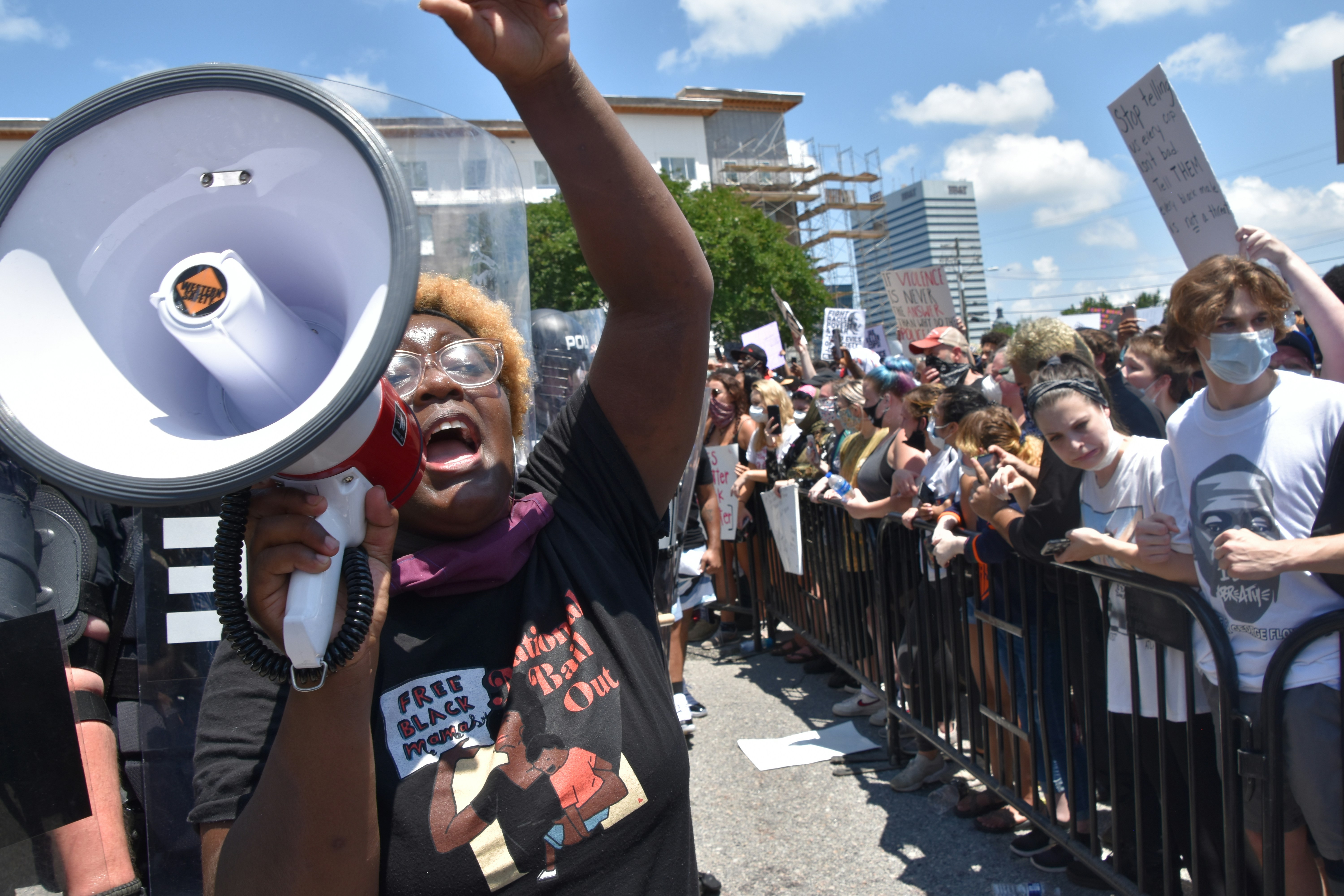 Activist passionately addressing a crowd with a megaphone during a protest, surrounded by supporters holding signs. The atmosphere reflects urgency and unity.