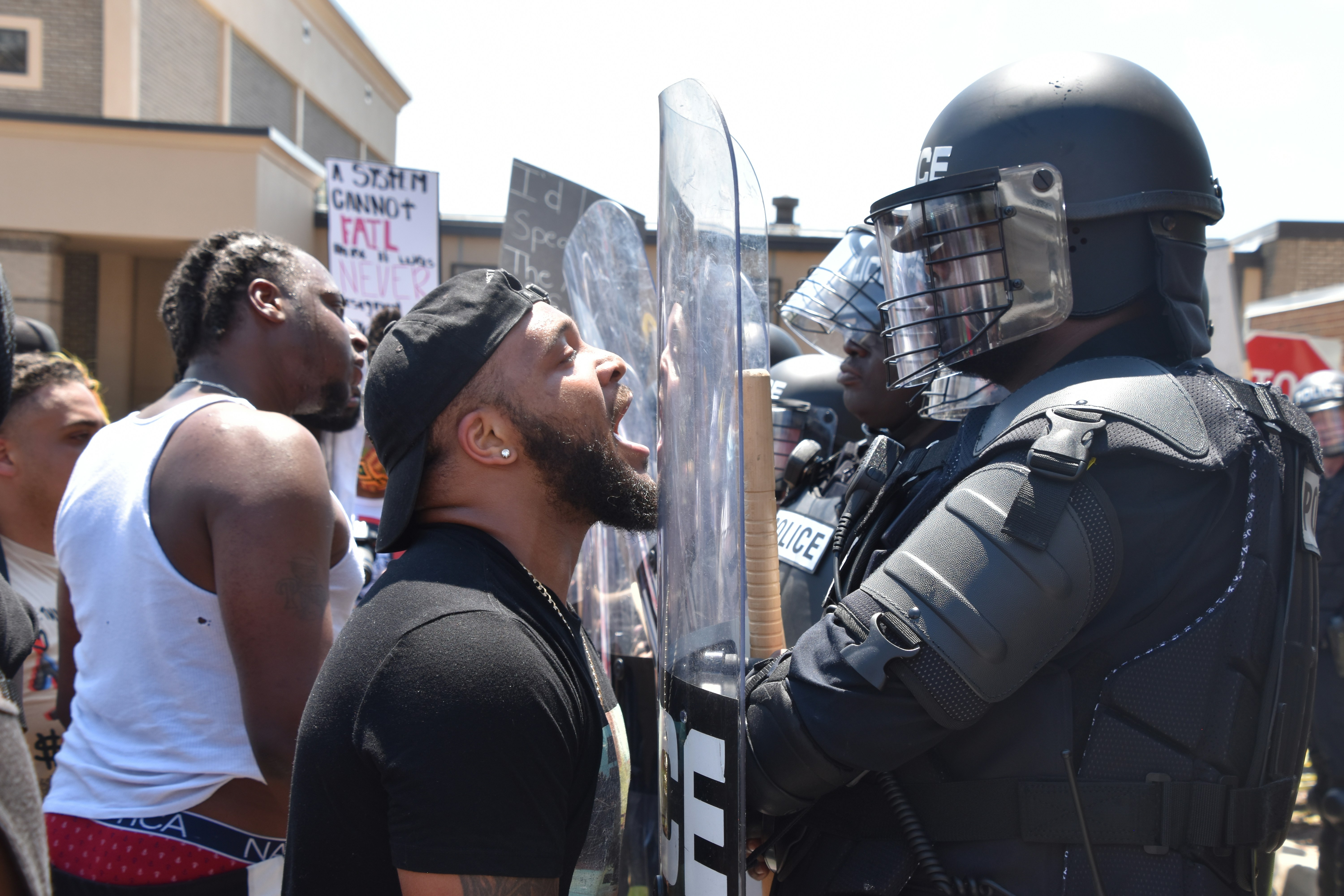 Protester faces off with riot police, both in tense standoff under bright daylight.