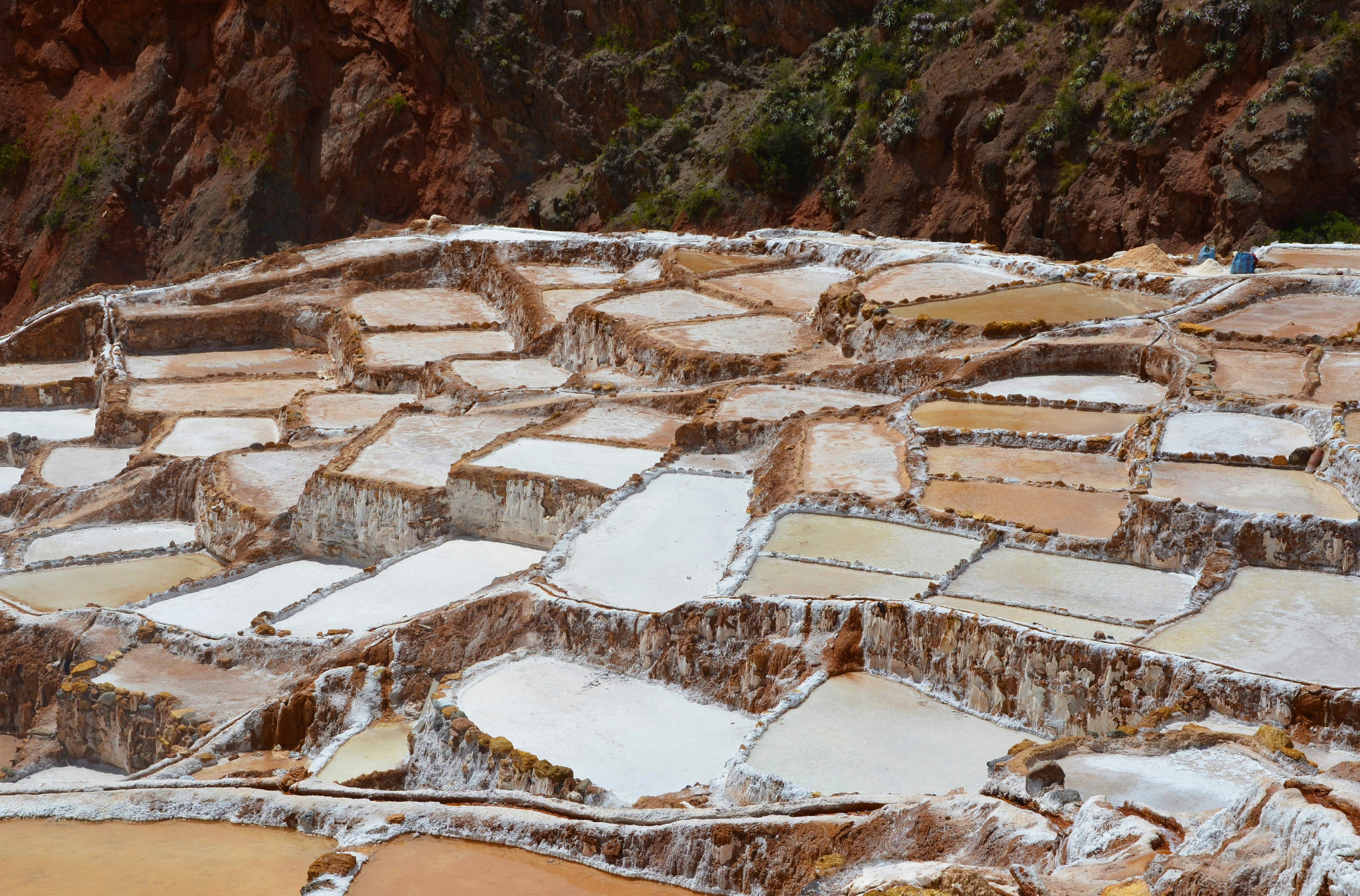 Intricate salt evaporation ponds arranged in terraces, showcasing a palette of earthy colors under bright sunlight.