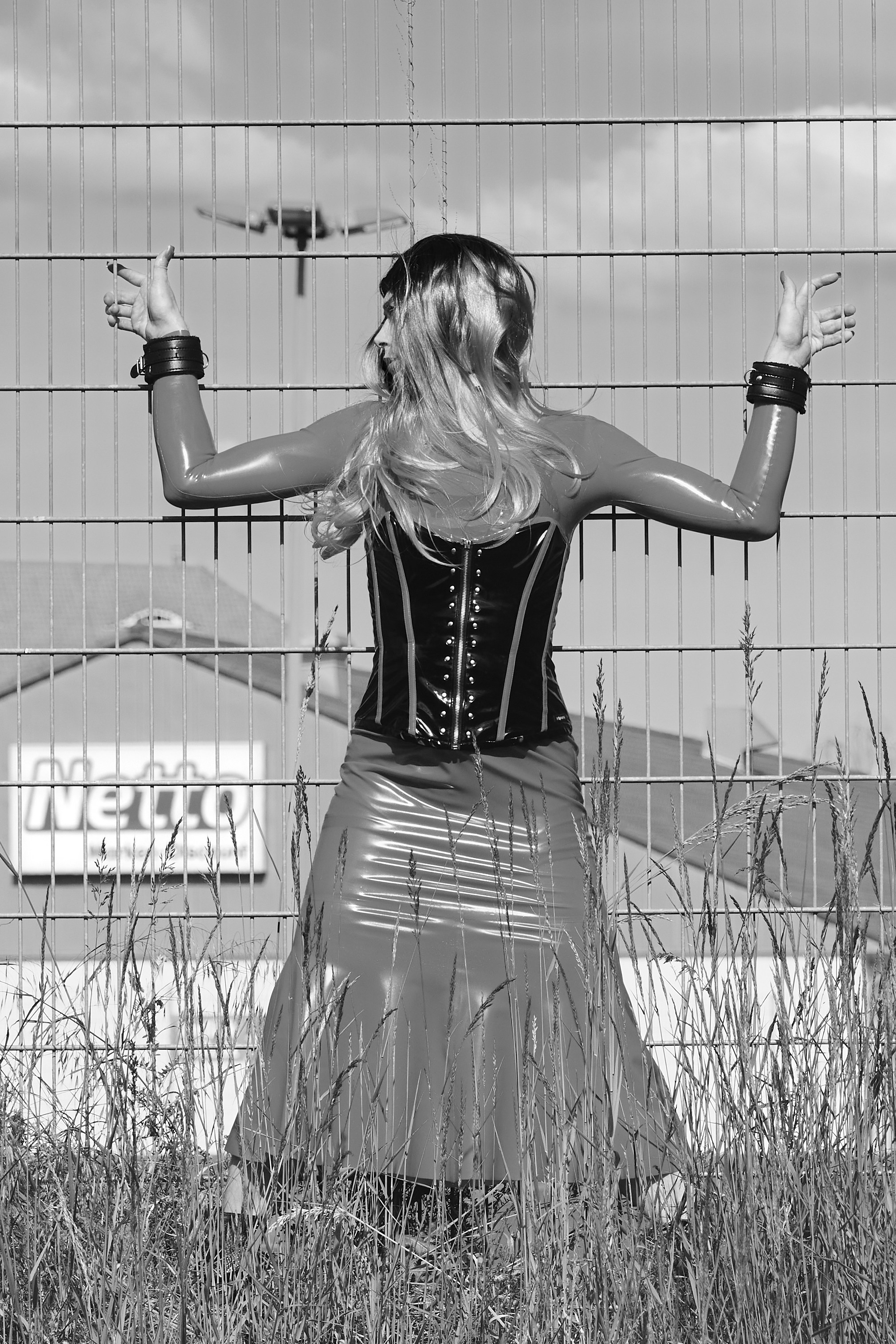 Corseted Silhouette: Windswept Portrait Behind a Chain-Link Fence