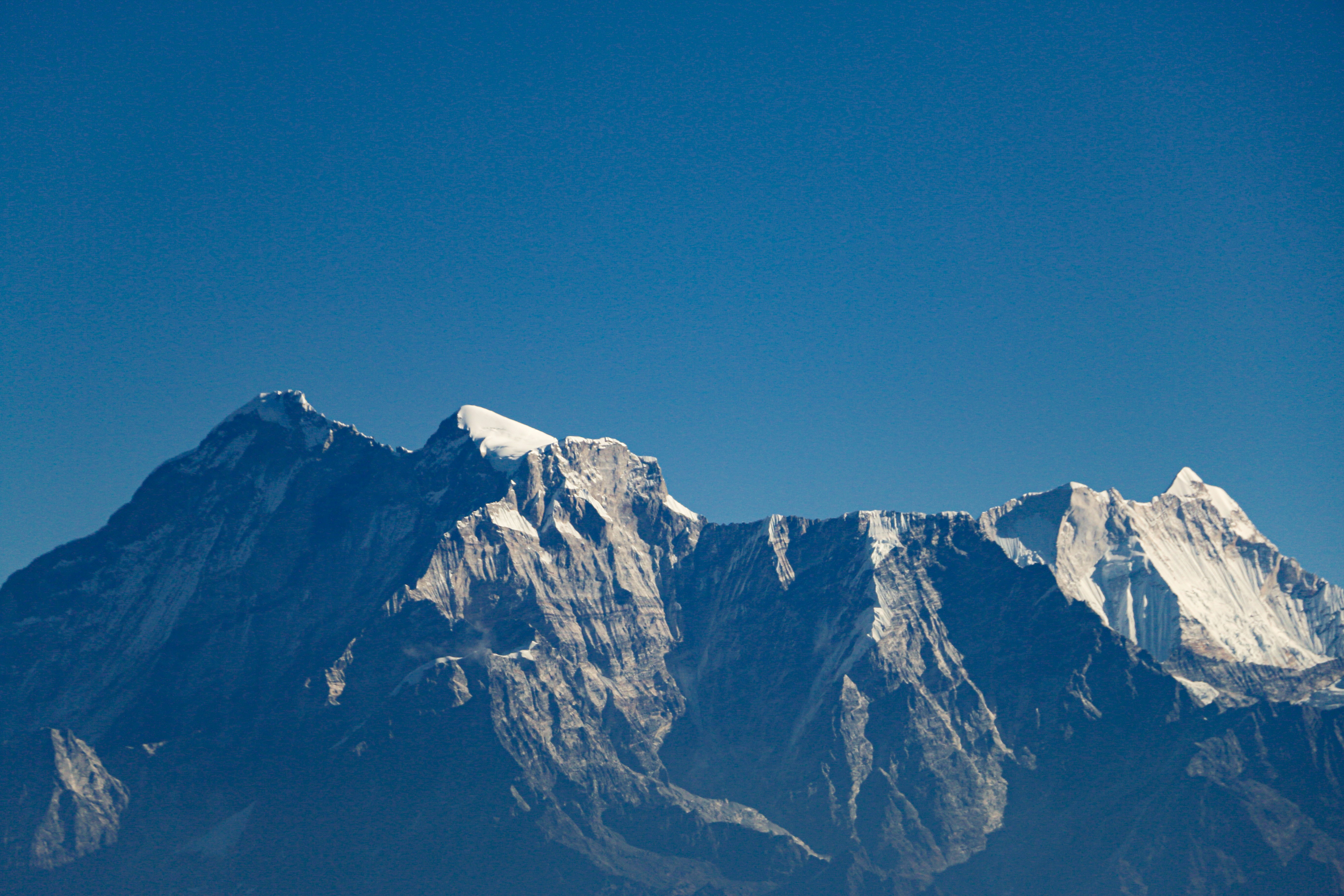 Snow-capped mountain range under a clear blue sky, showcasing rugged terrain and dramatic cliffs.