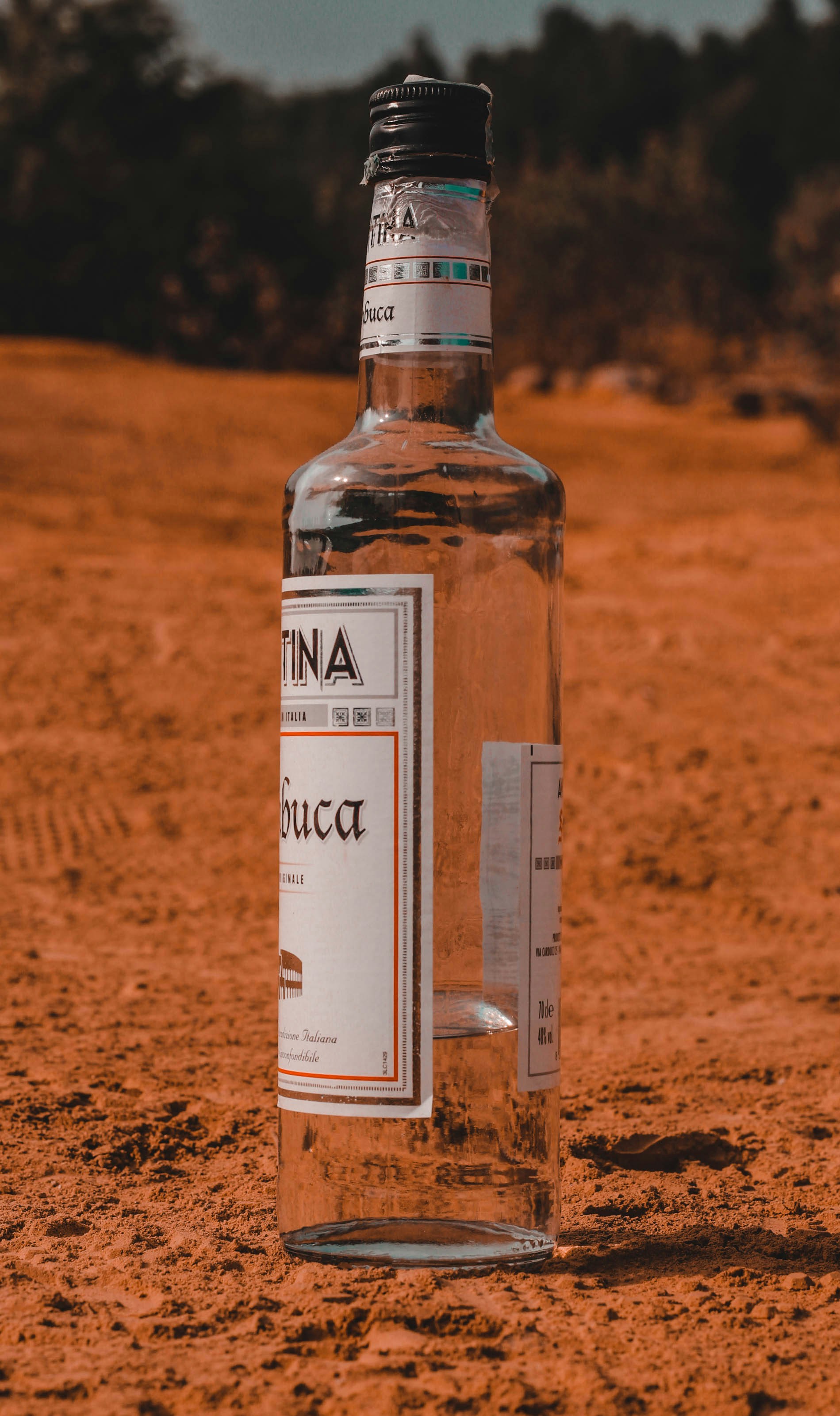 A bottle of alcohol sitting on the ground photo – Free Brown Image on ...