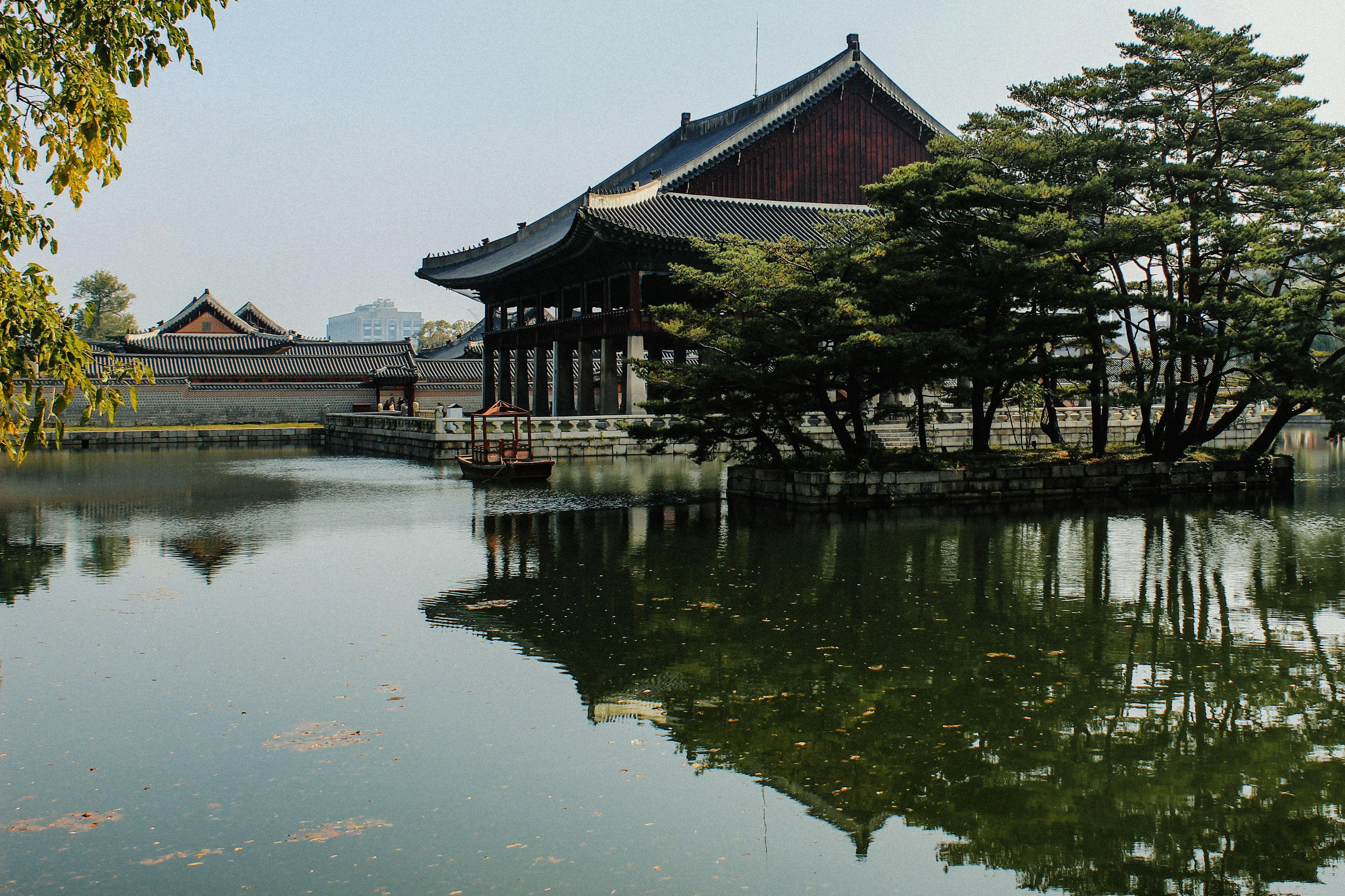 Traditional Asian architecture reflected in a serene pond, surrounded by lush greenery. The tranquil scene invites contemplation.