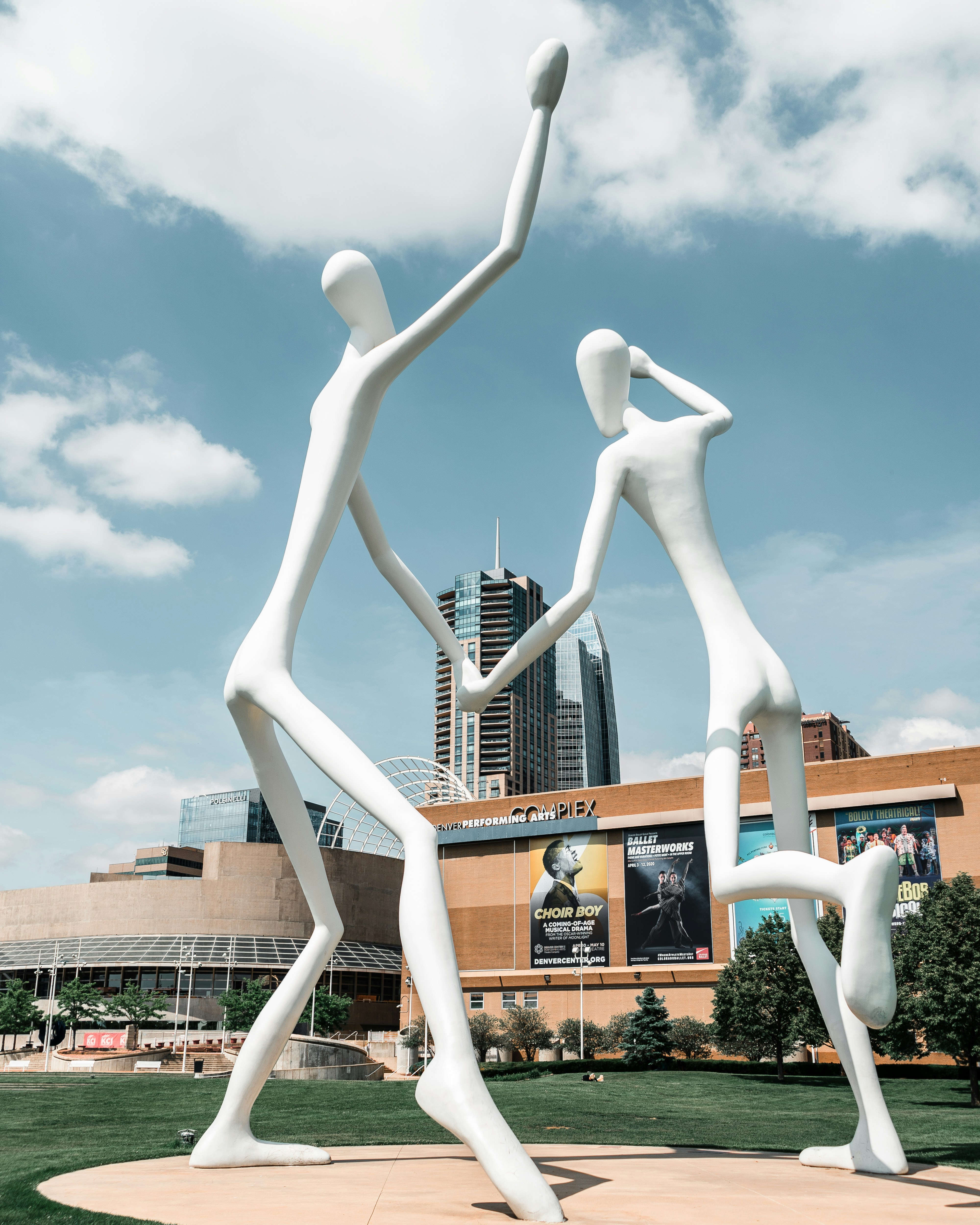 Two abstract figures in white, holding hands, embodying connection and movement against a vibrant urban backdrop.