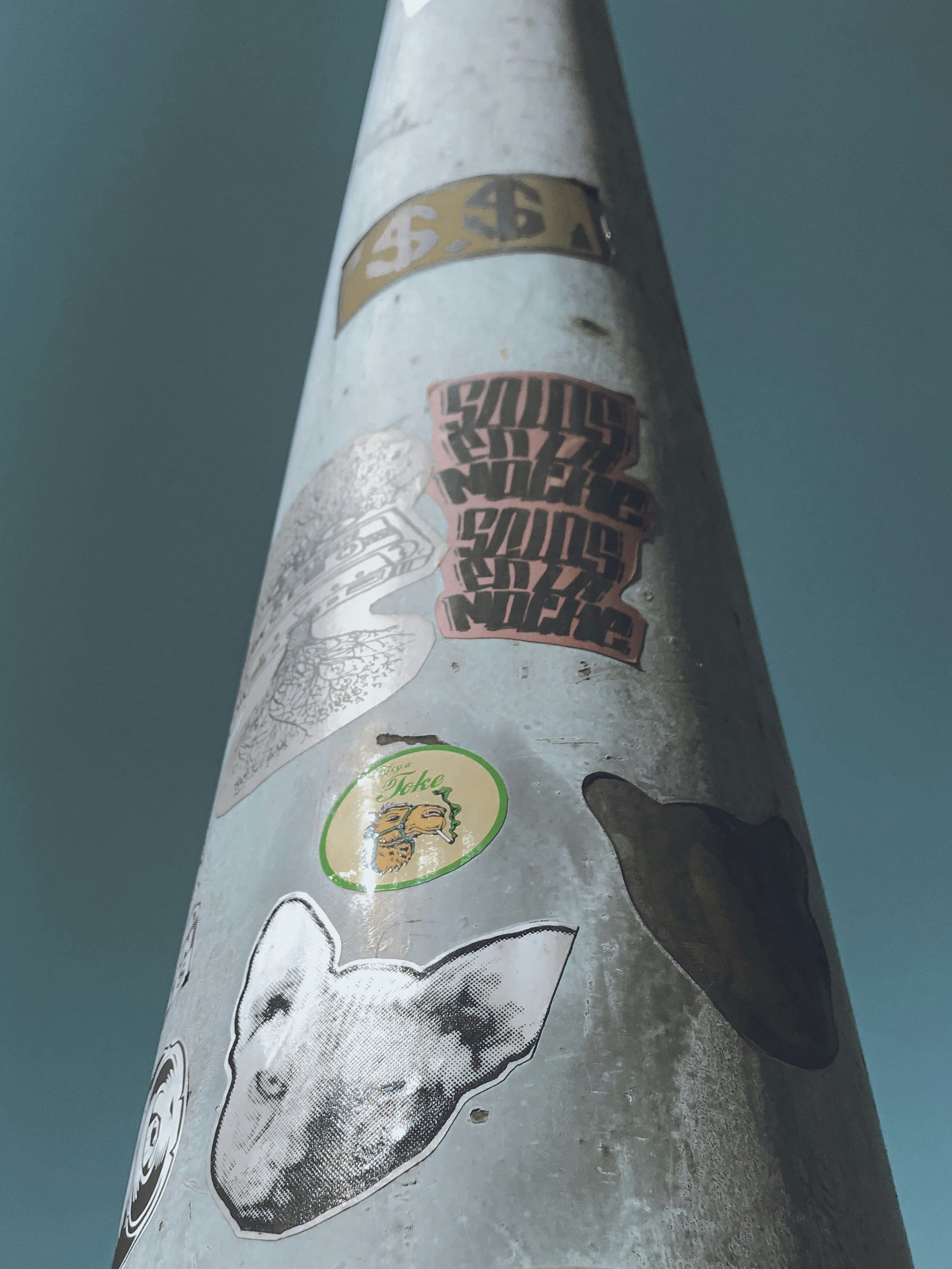 Stickered Monolith: A Decal-Painted Pole Reaching Toward a Blue Sky