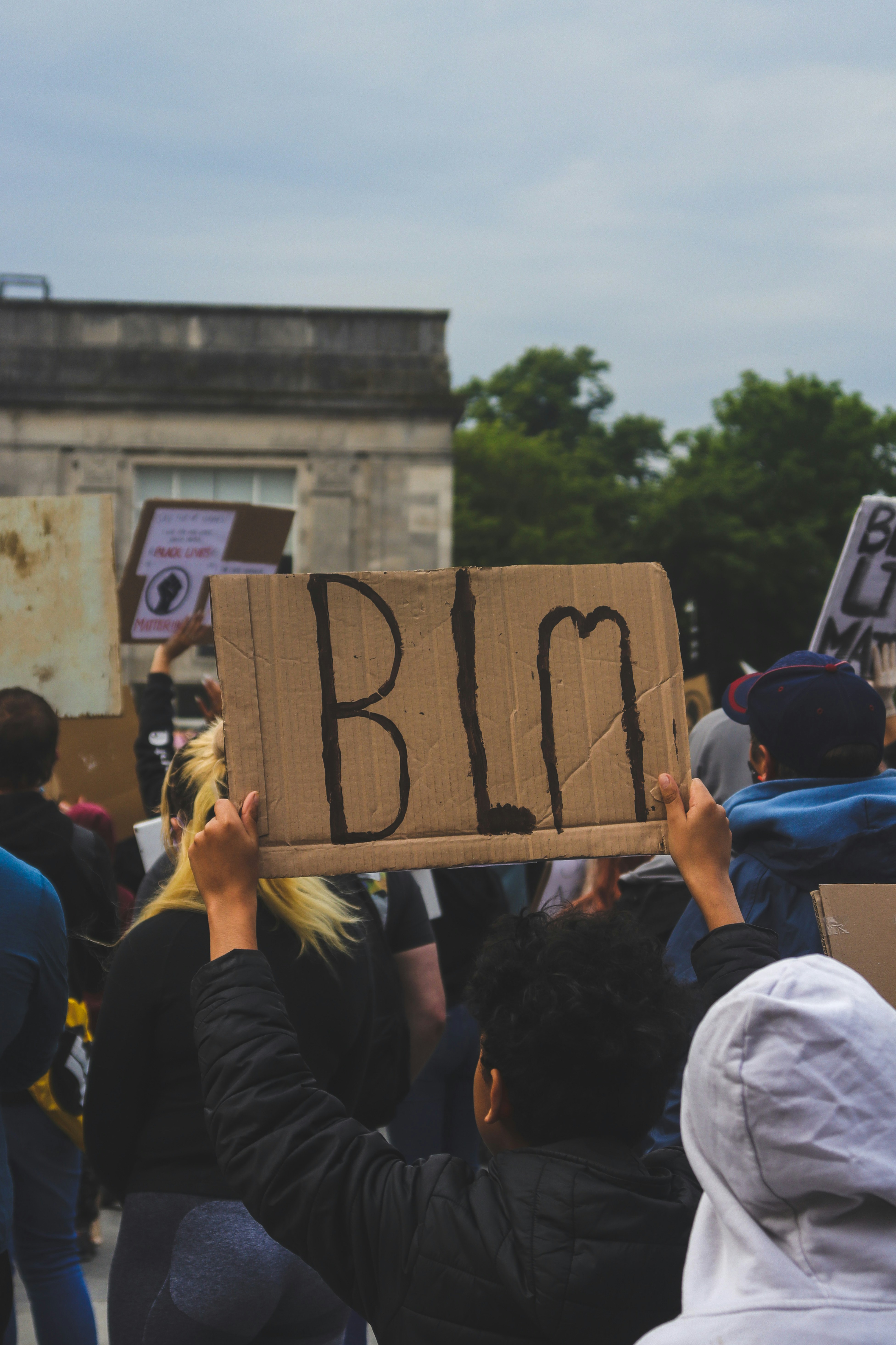 Centerframe Banner: The 'BLM' Cardboard Sign Rises Over a Crowded Protest