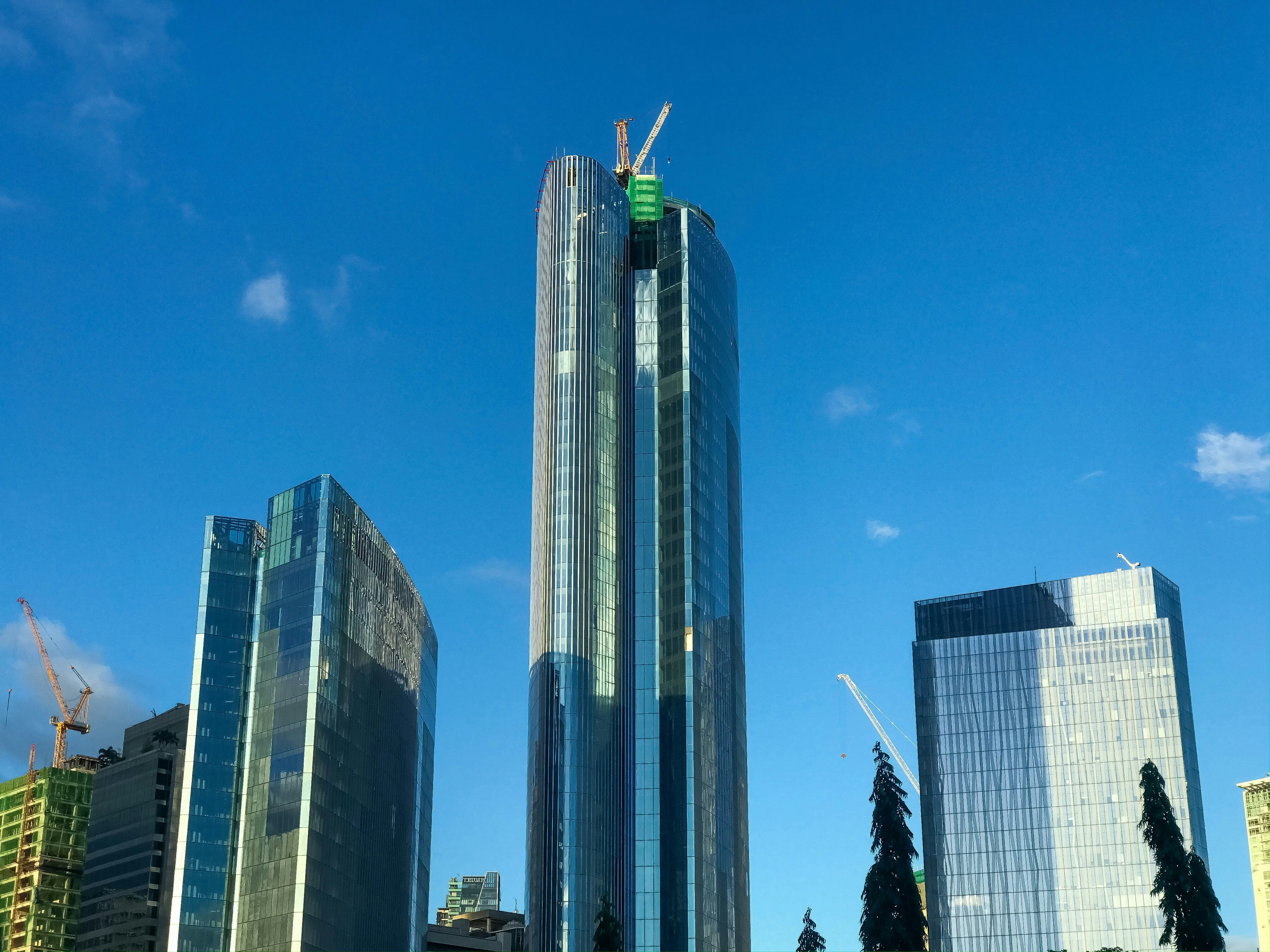 Modern skyscrapers rise against a bright blue sky, with a central tower under construction.