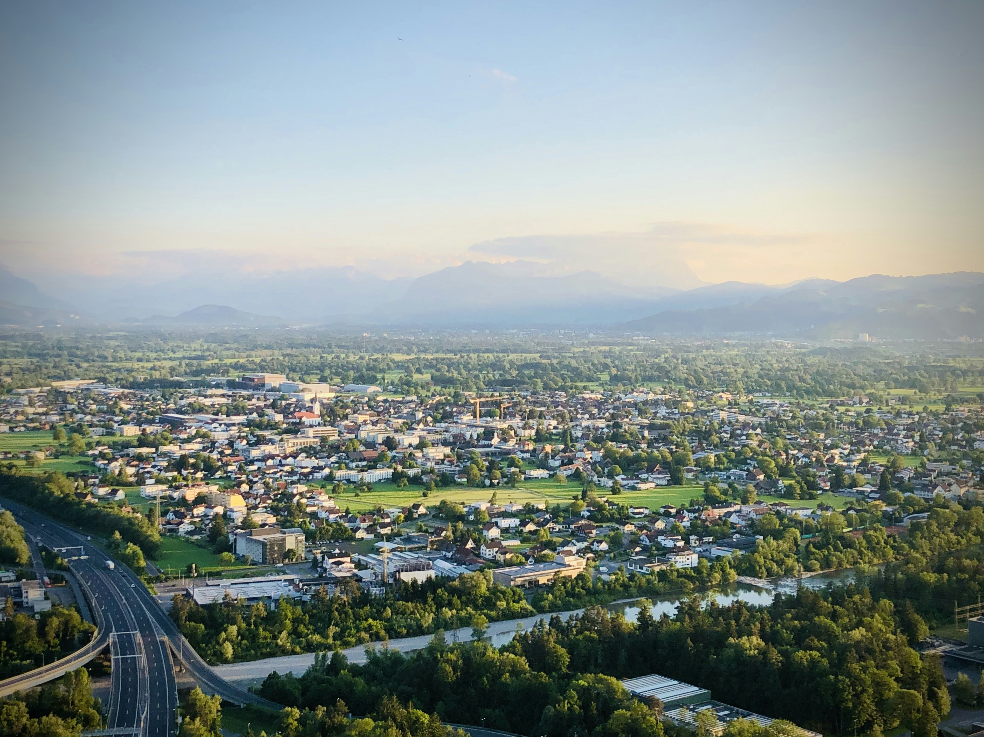 A city surrounded by lush greenery and mountains under a clear blue sky.