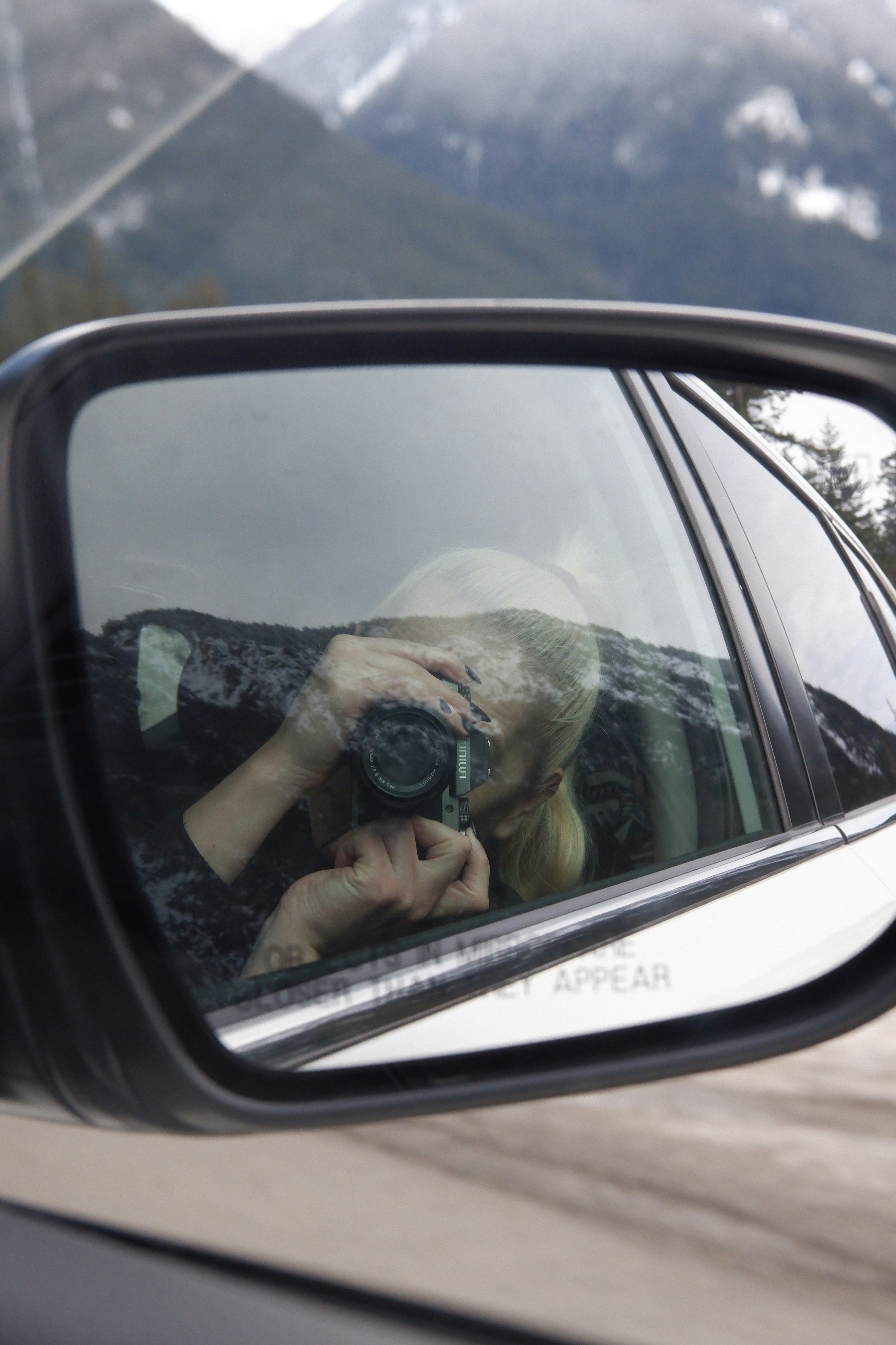 Mirror Portrait: A Photographer Reflected in the Car Side-View with Mountain Backdrop