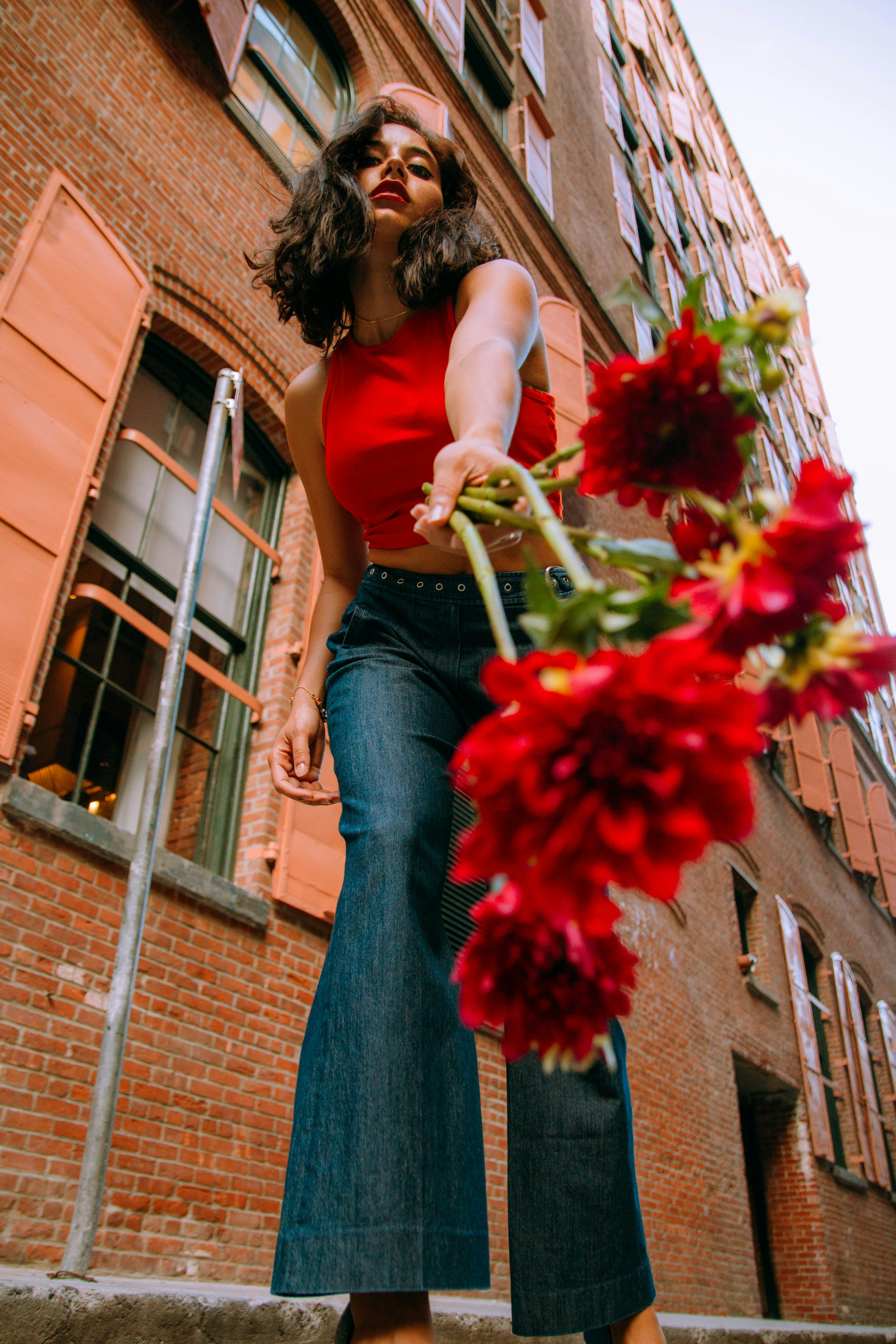 Woman in red tank top and blue denim jeans holding red bouquet of ...