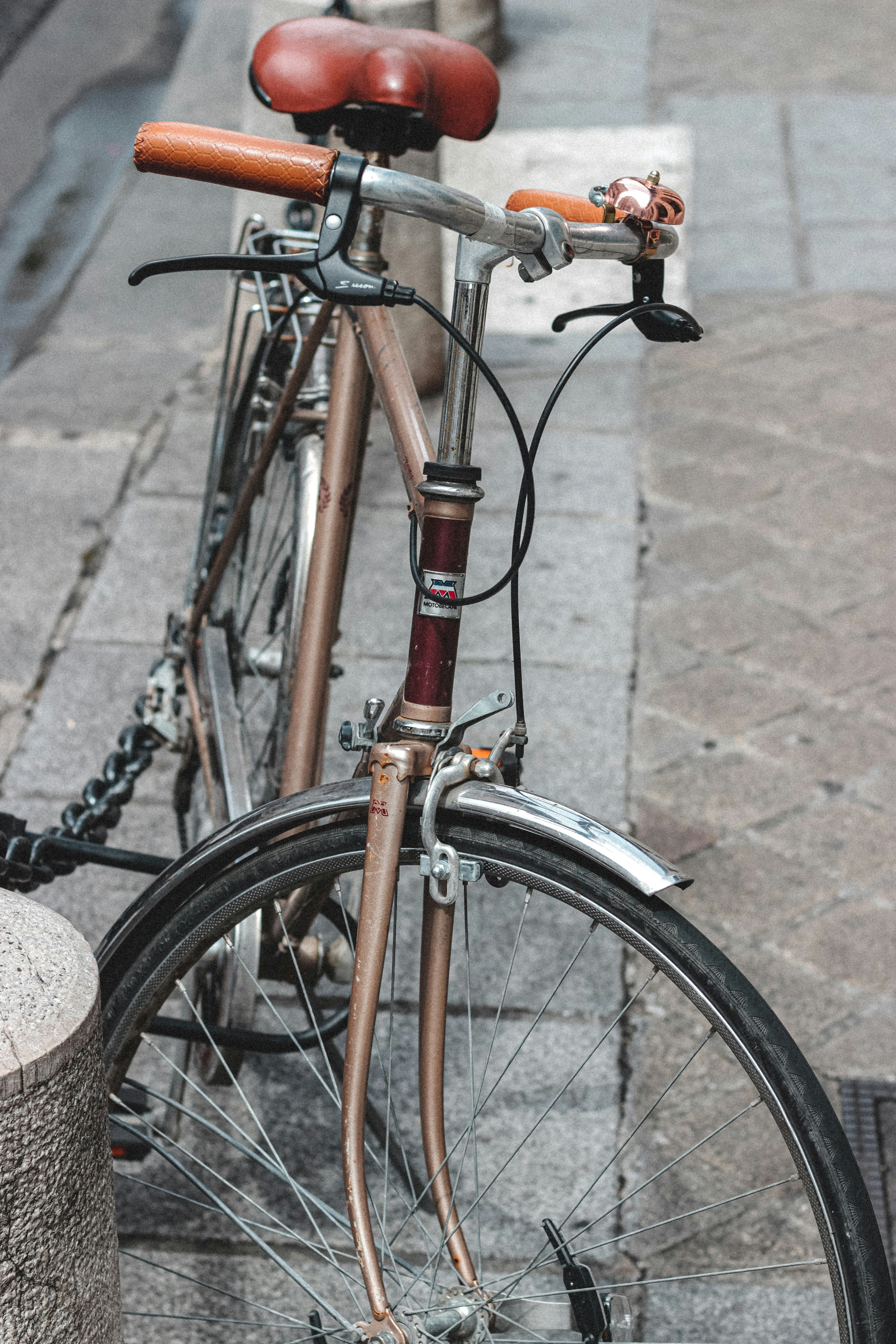 A classic bicycle rests against a stone pillar on a cobblestone street, showcasing its worn handlebars and retro design.