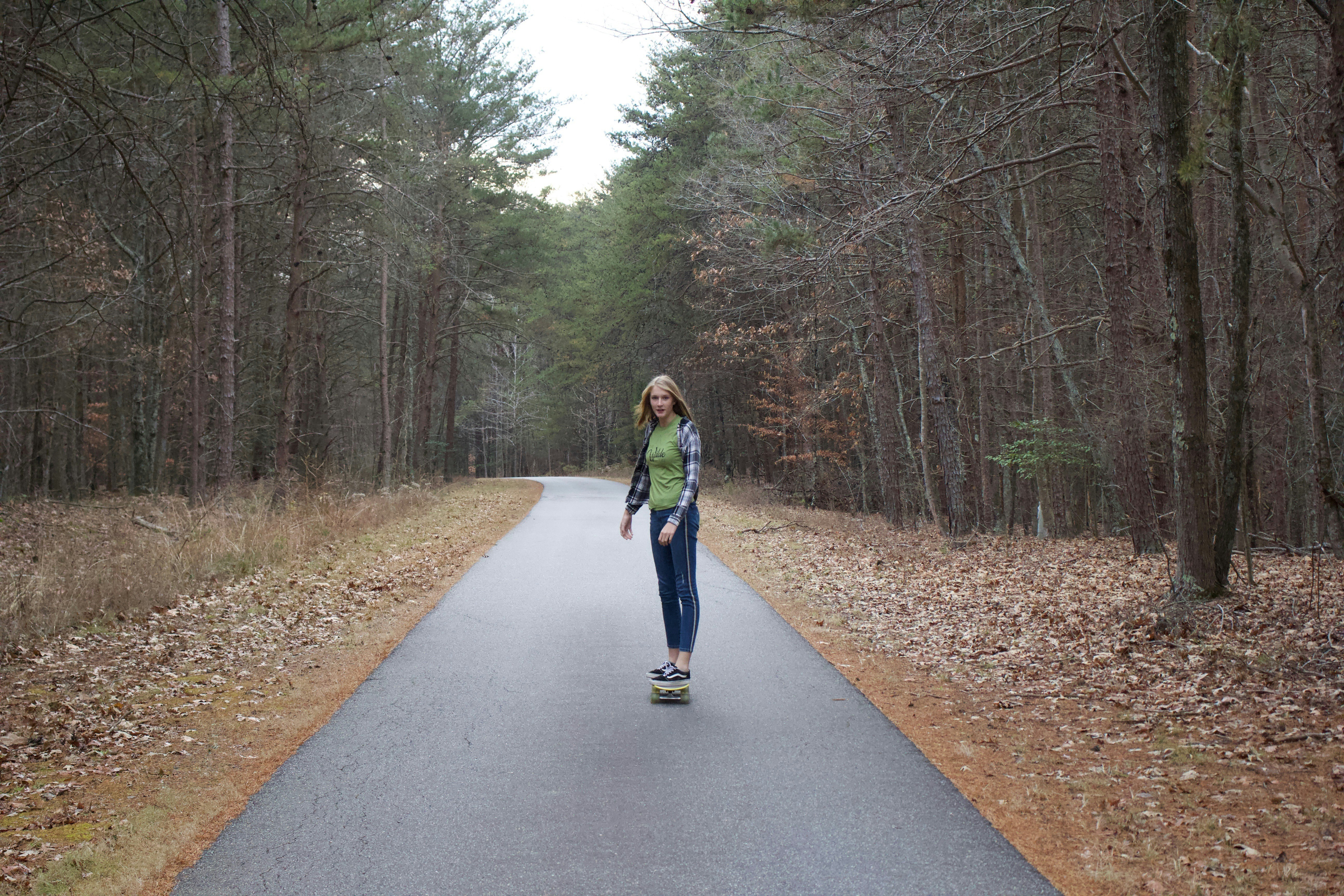 woman in blue jacket standing on gray asphalt road between trees during daytime