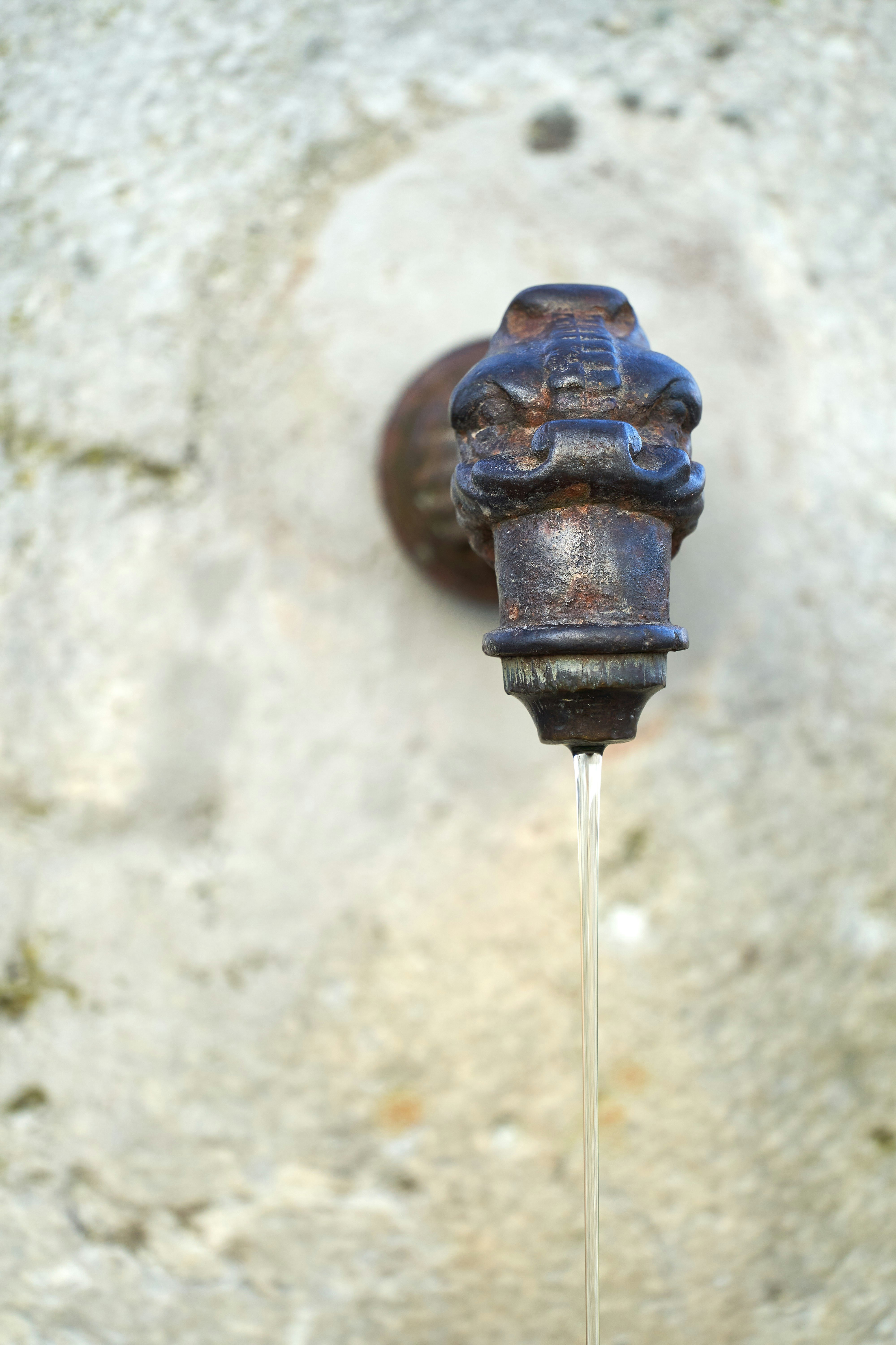 Rusted Spigot with a Single Thread of Water Against Weathered Concrete