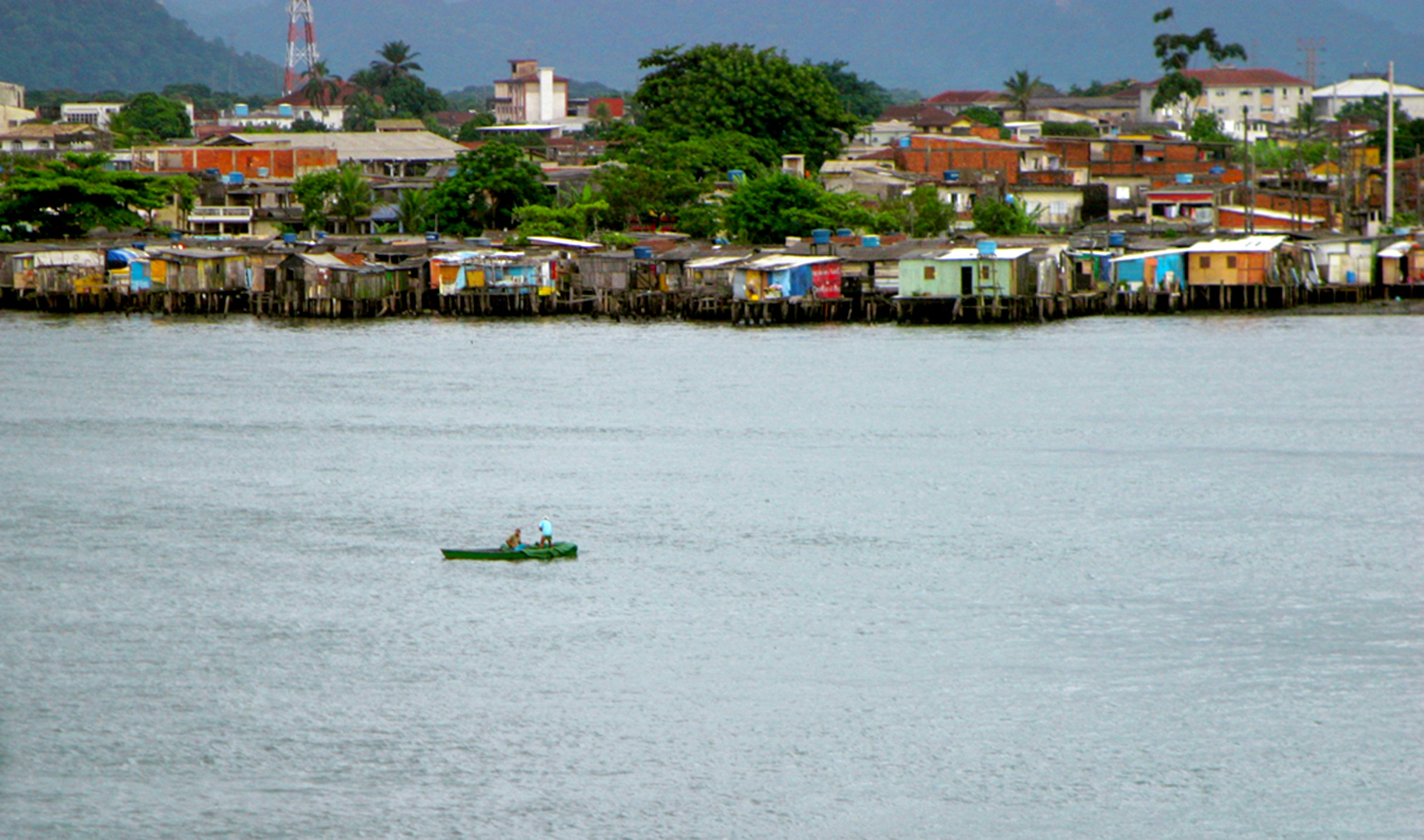 Green boat glides on calm water near colorful coastal houses during daytime.