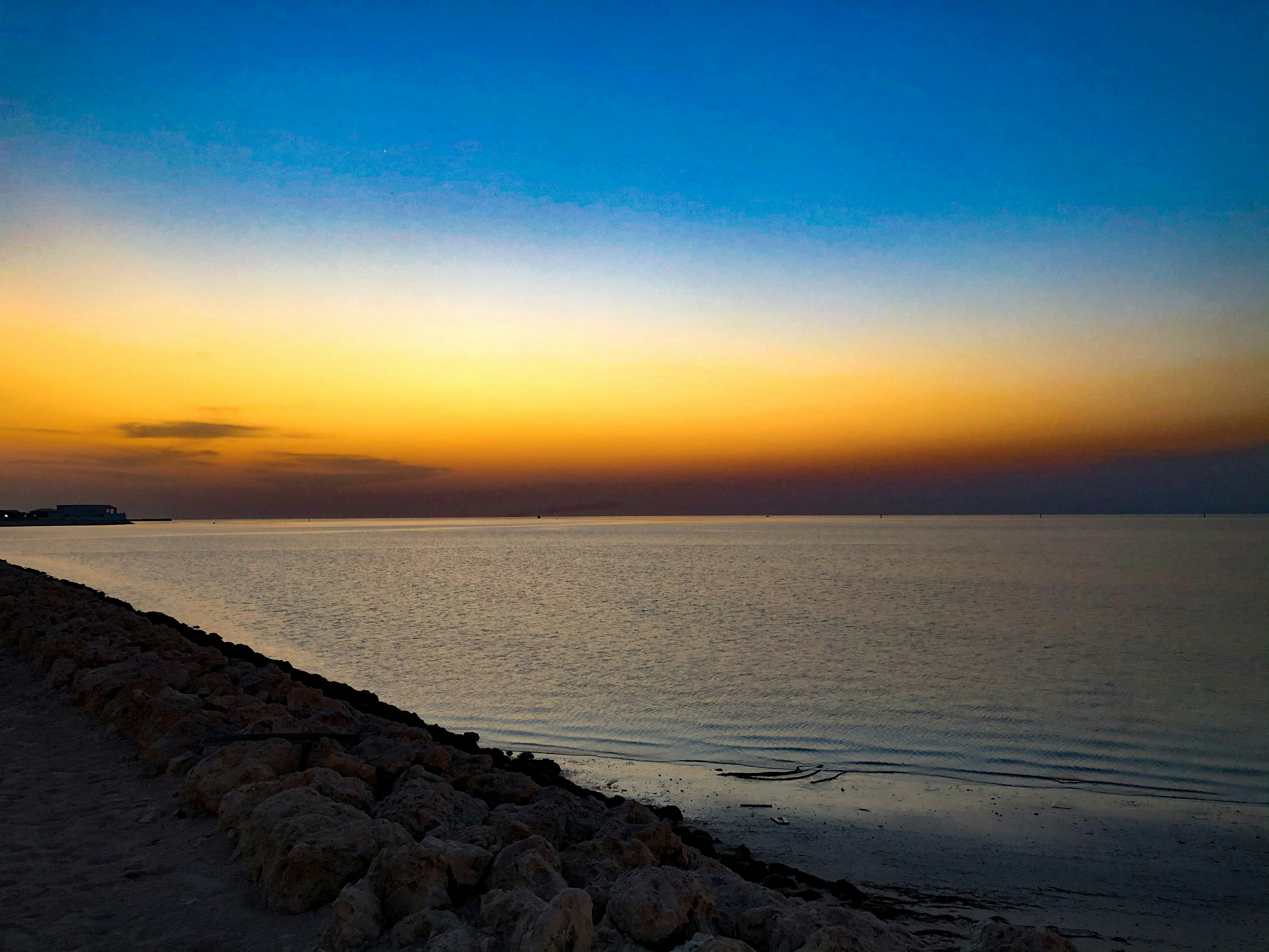Vibrant sunset over a calm sea with a rocky shoreline silhouetted against the gradient sky.