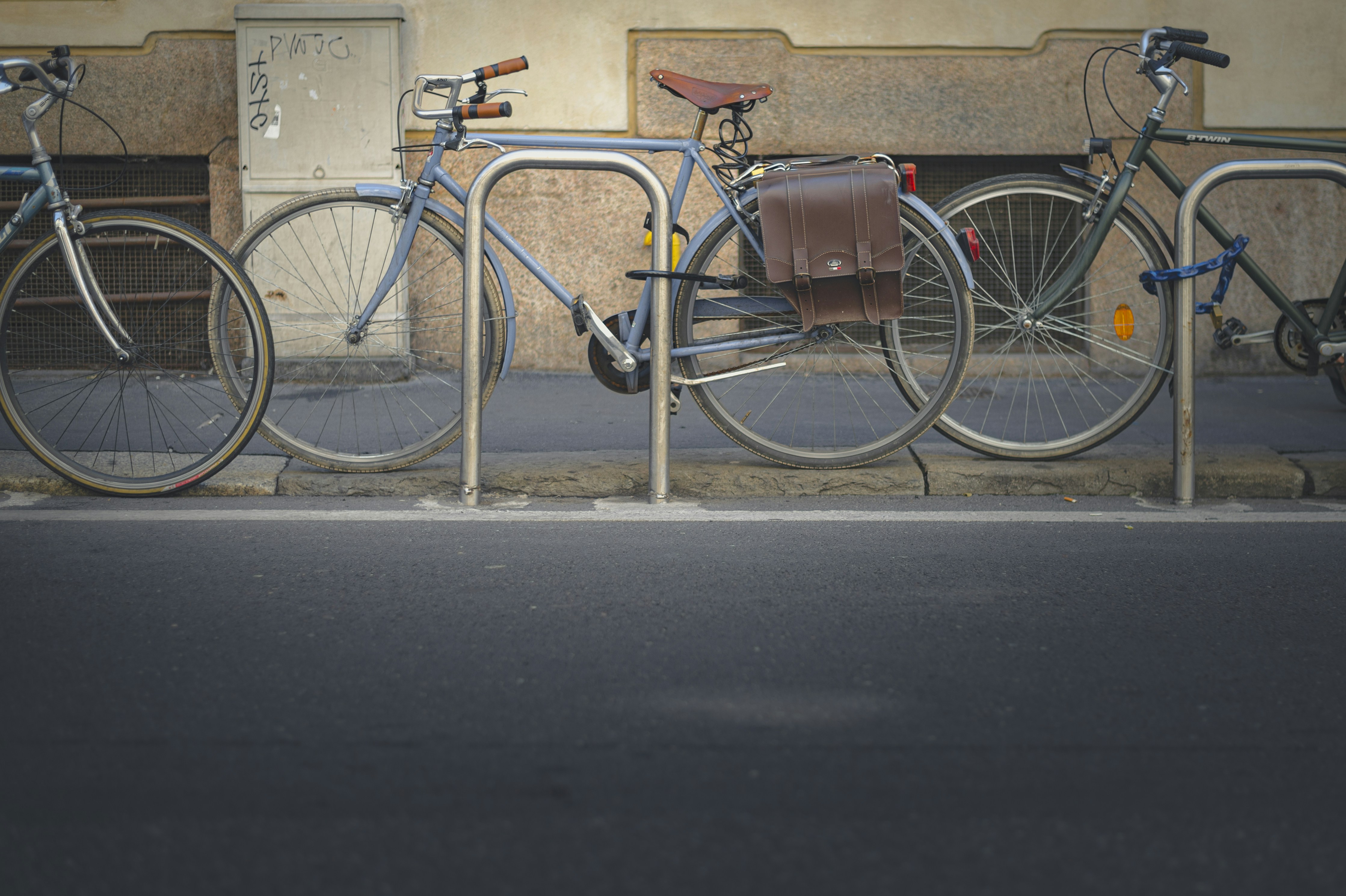 A row of bicycles secured to a railing in an urban setting, showcasing their contrasting designs and a leather bag on one bike. 