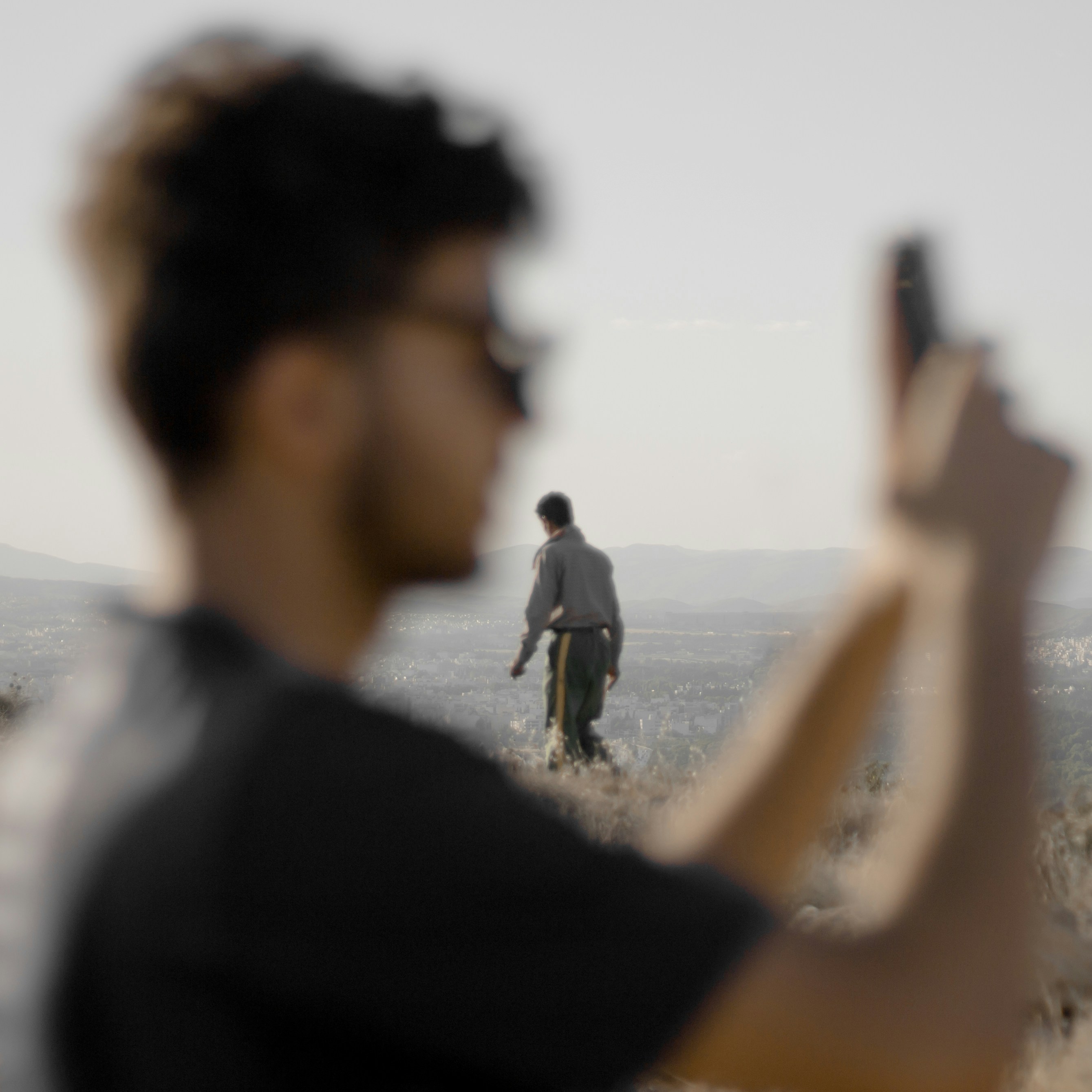 Horizon Steps: A distant walker crosses a sunlit desert while a friend records the moment.