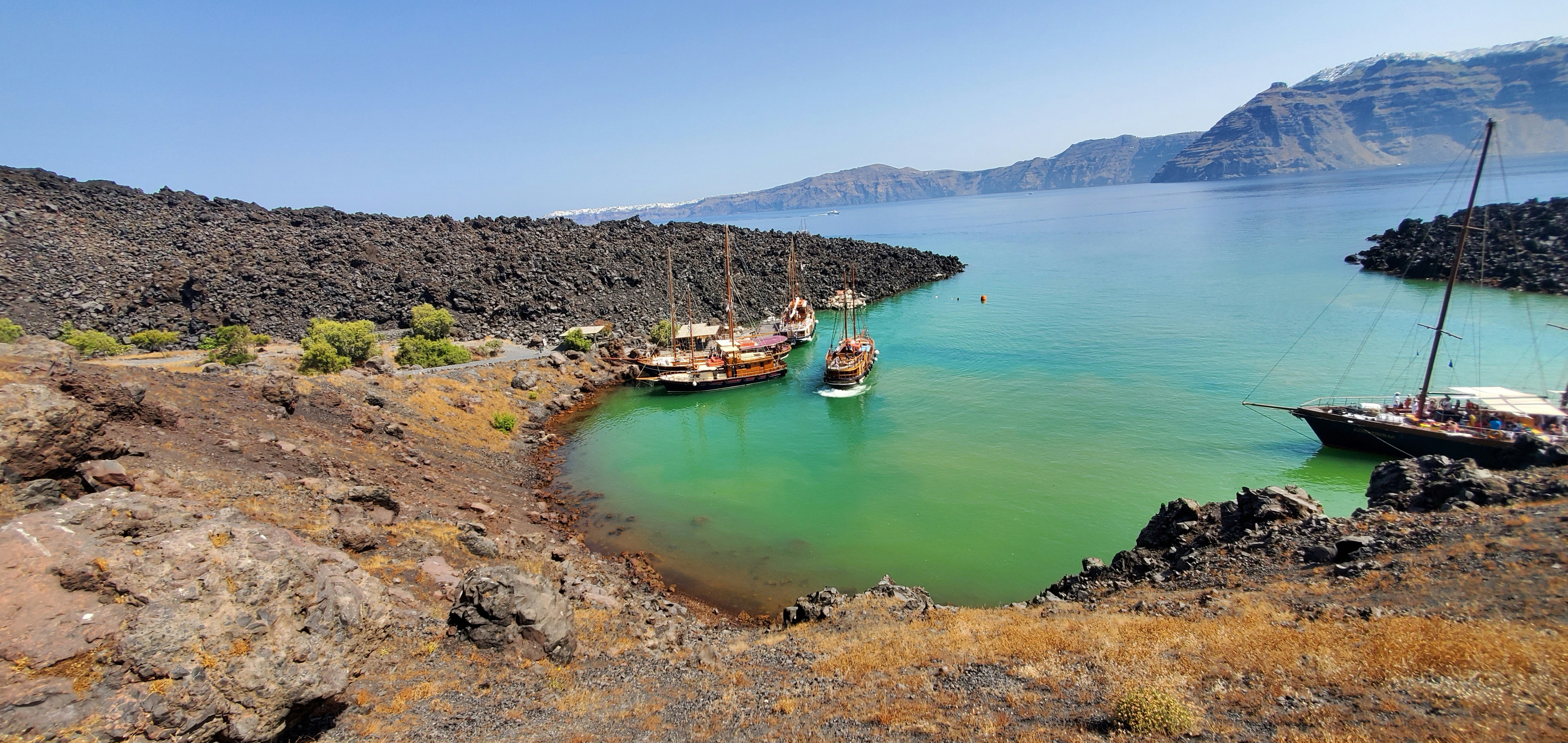 Wooden boats anchored in a cove surrounded by volcanic rock and turquoise waters on a clear day.