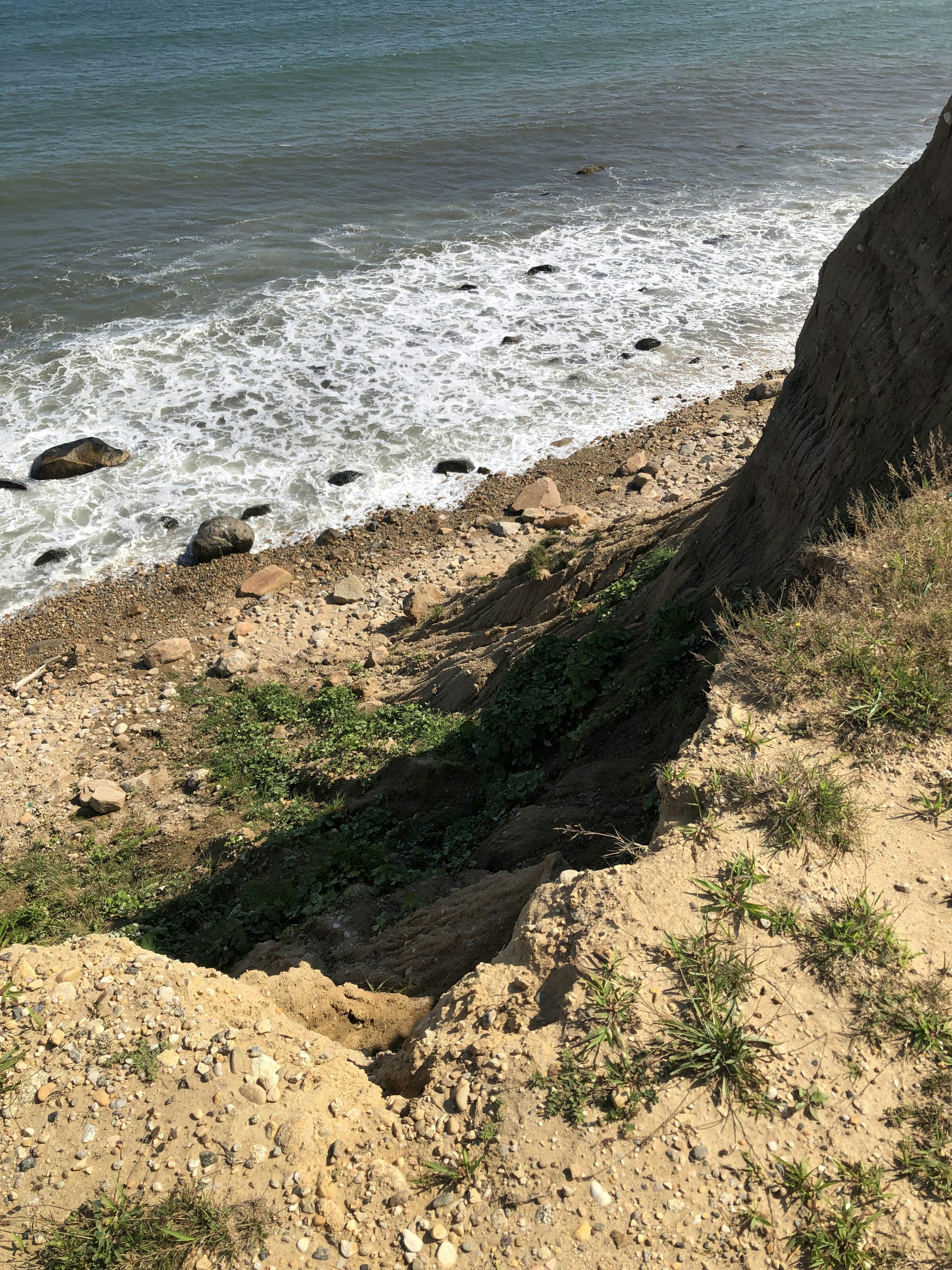 Edge of Erosion: Sunlit Cliff Overlooking a Pebbled Shore