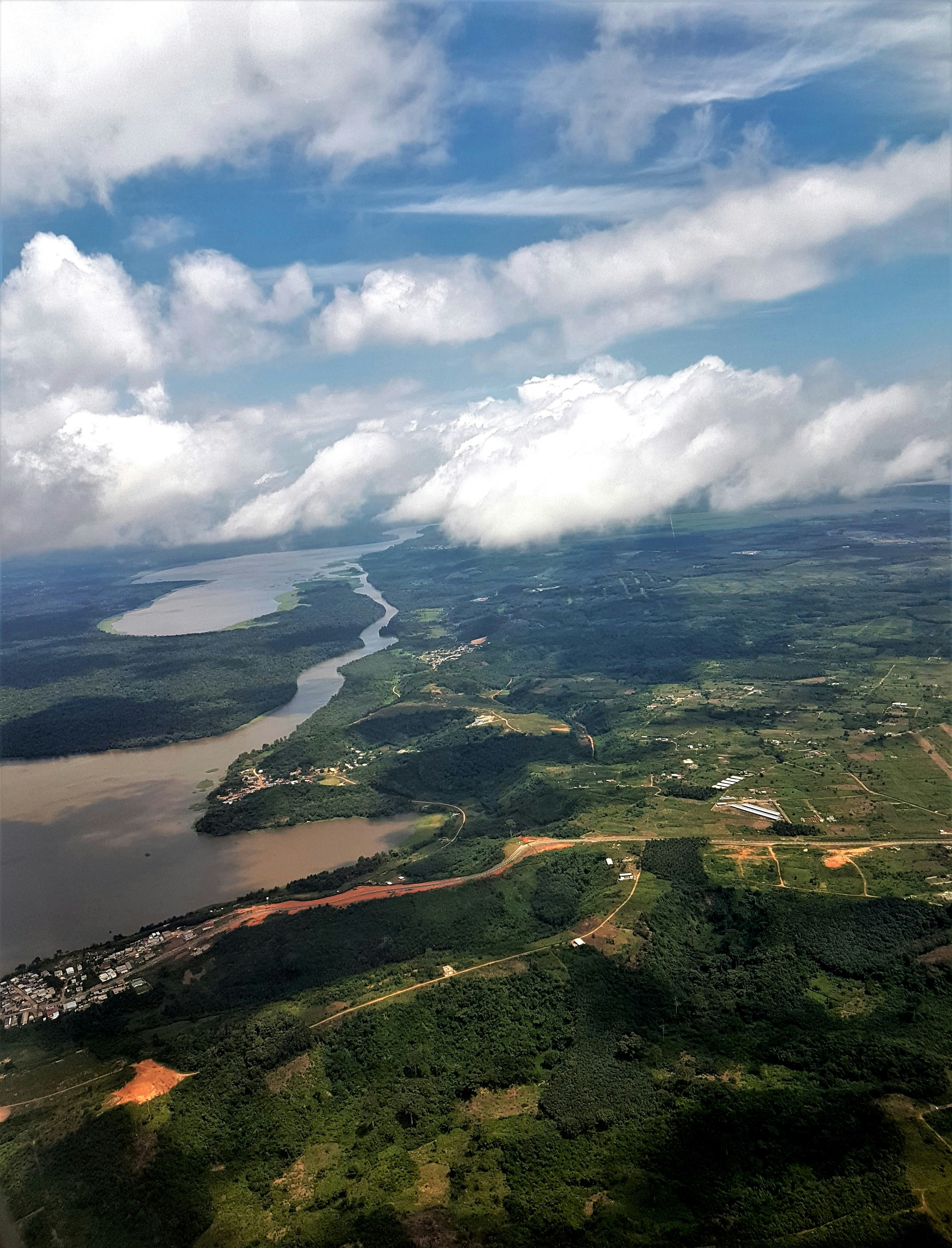 Aerial view of a winding river flowing through lush green landscapes under a dramatic sky with scattered clouds.