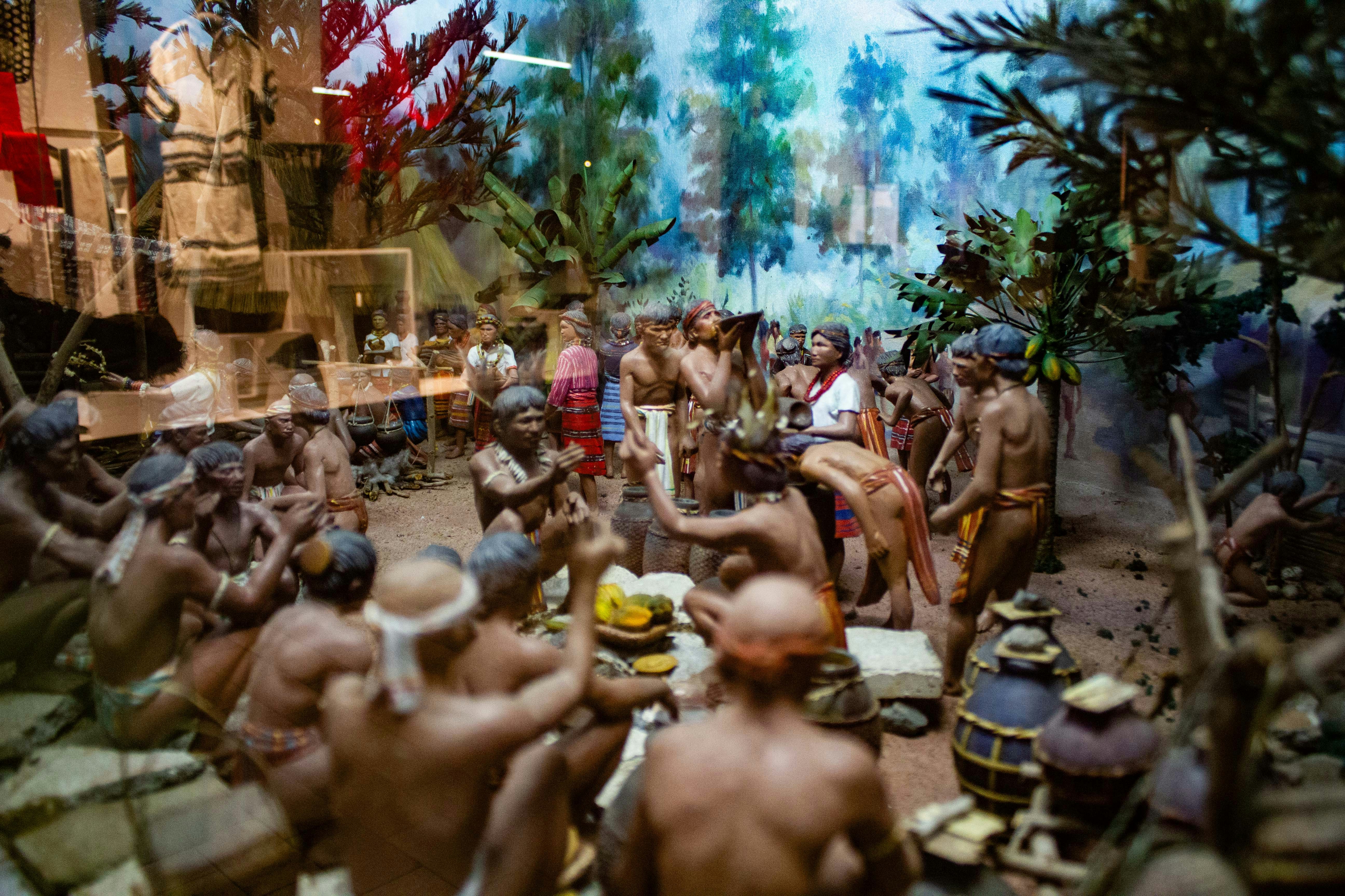 Detailed diorama depicting a historical scene with numerous figures engaged in communal activities surrounded by lush foliage.