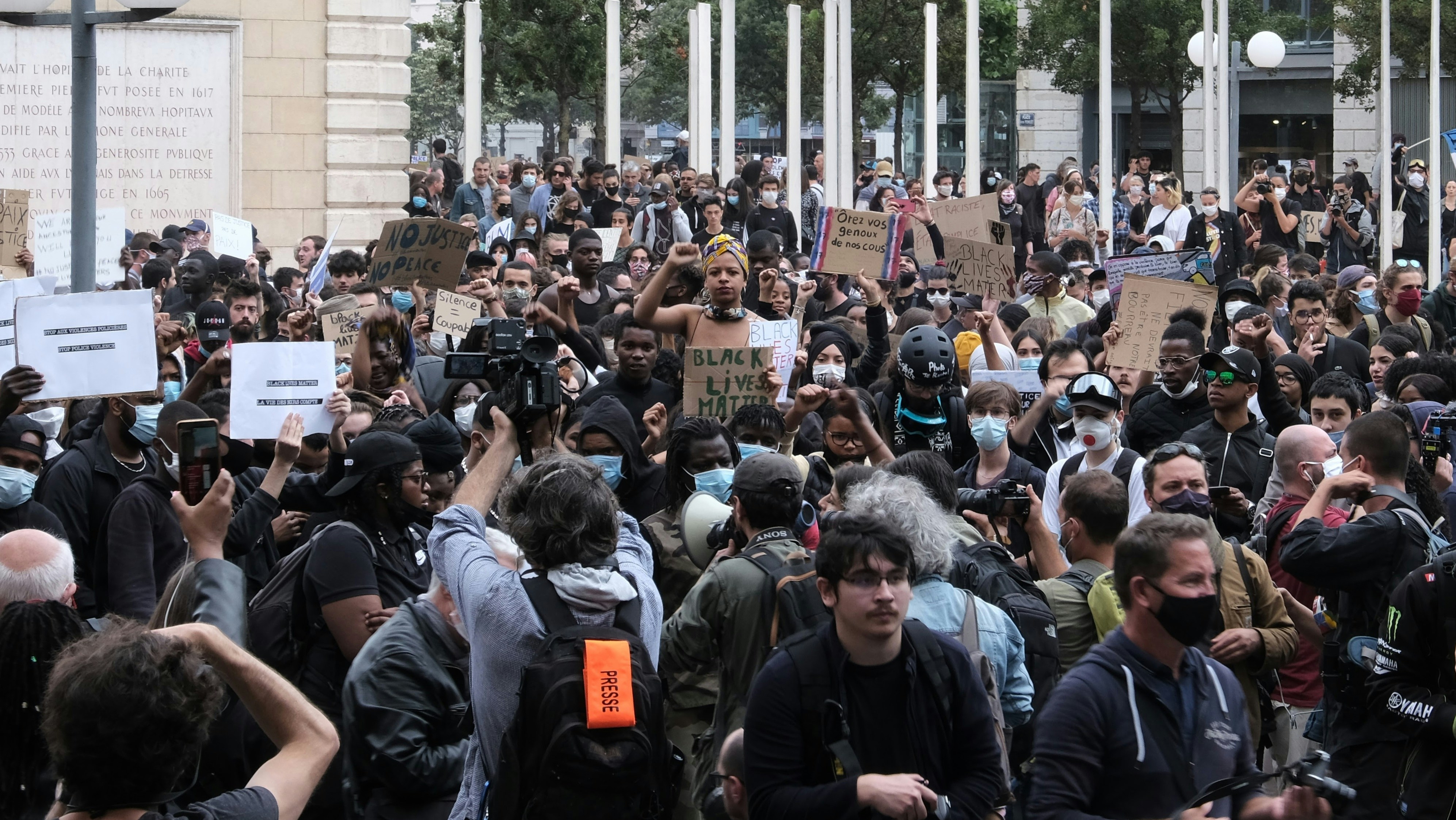 Crowd of protesters holding signs, gathered in a city square amidst tall columns.