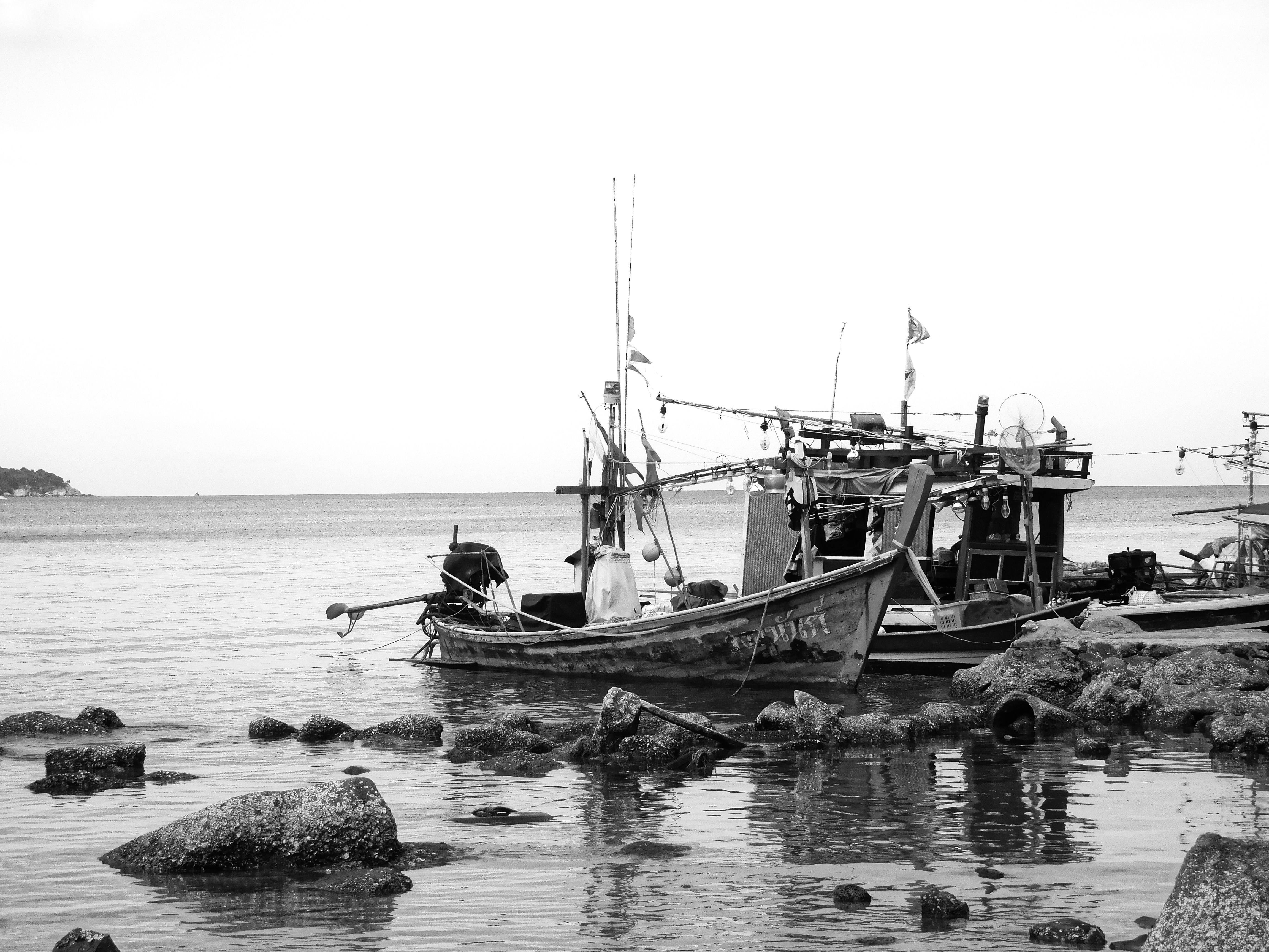Fishing boats anchored near rocky shore under a cloudy sky.