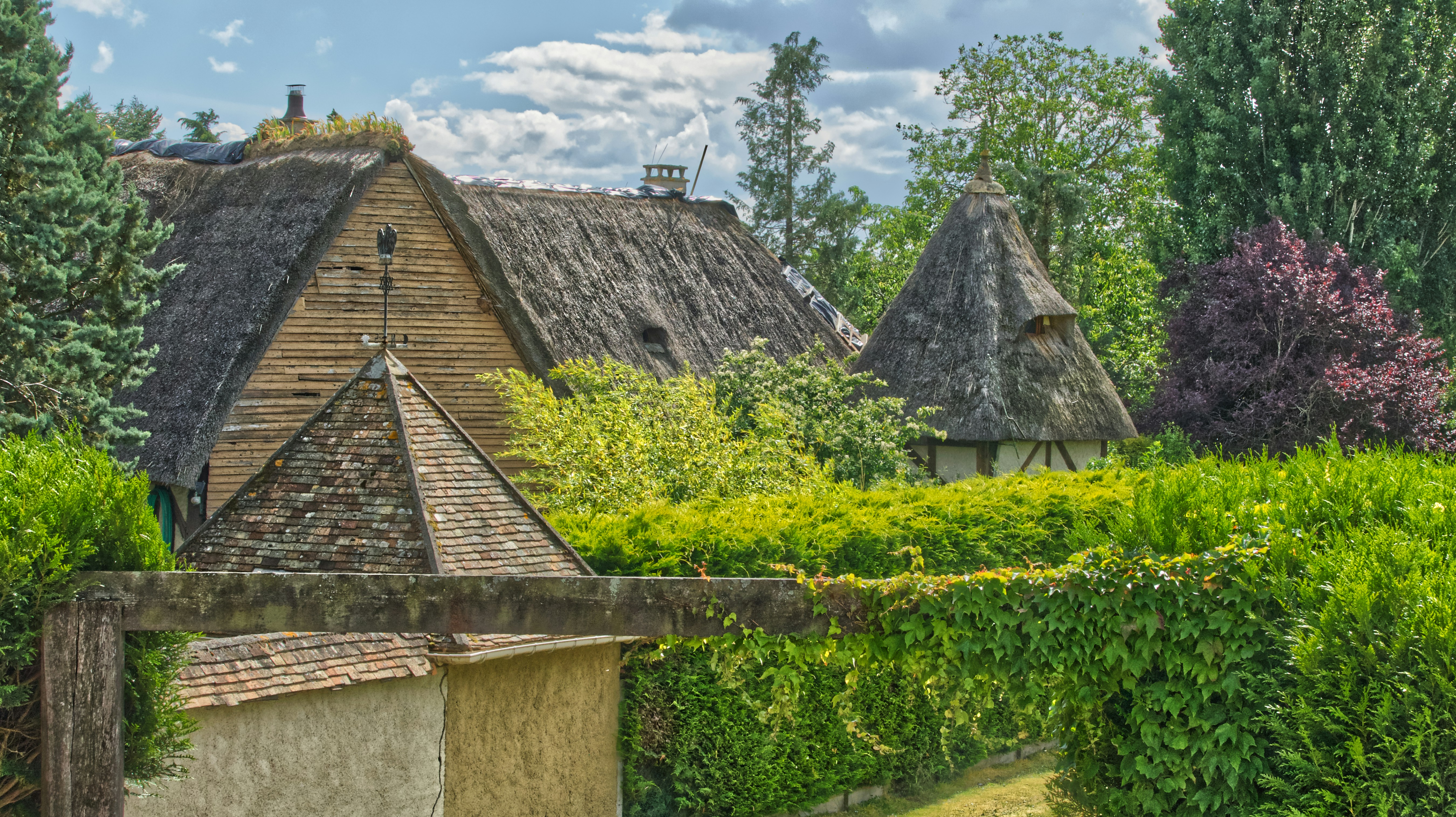 Charming thatched-roof cottages nestled among lush greenery under a bright sky. The scene evokes a sense of tranquility and rustic elegance.