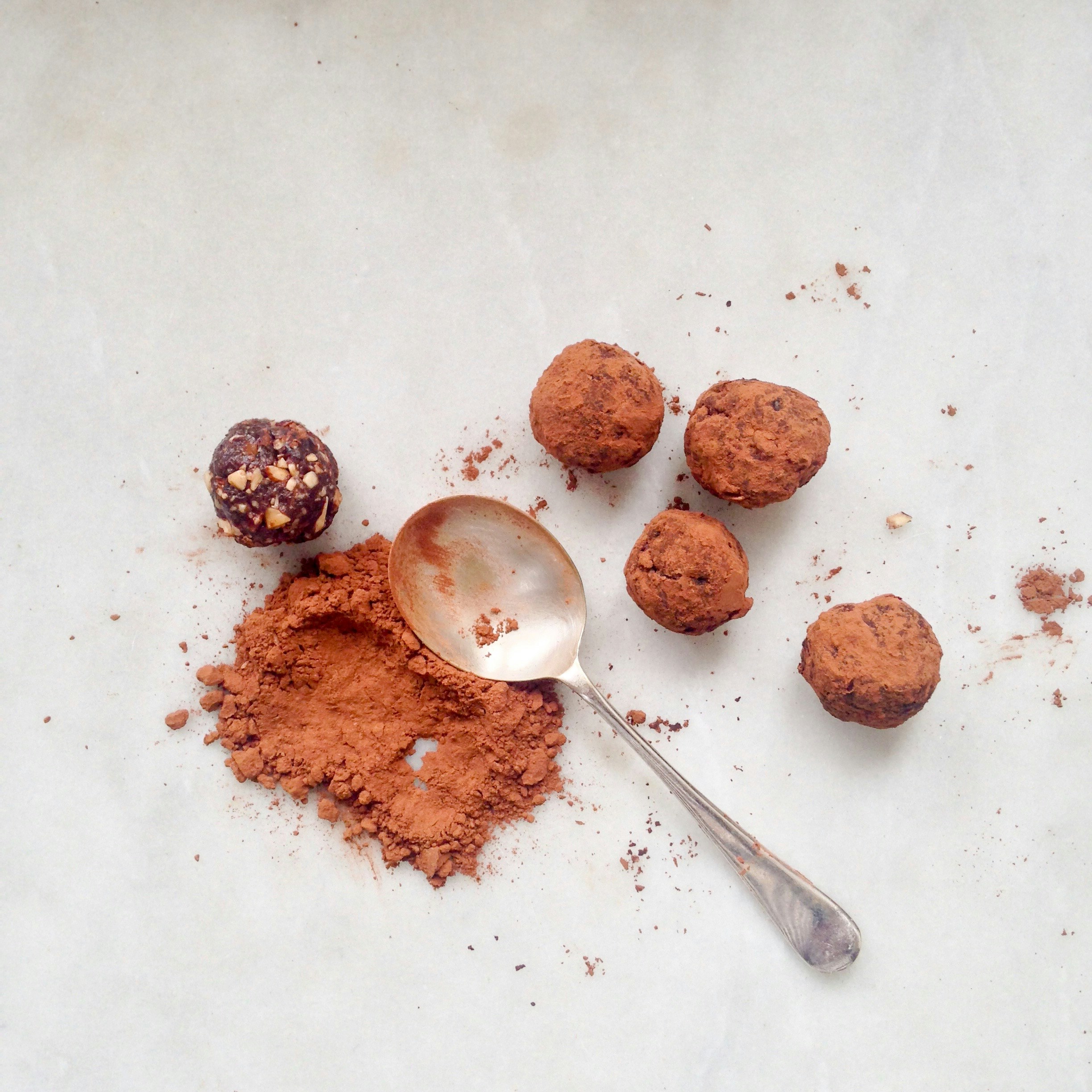 Chocolate truffles scattered on a marble surface with cocoa powder and a silver spoon. A rich arrangement showcasing the art of confectionery.