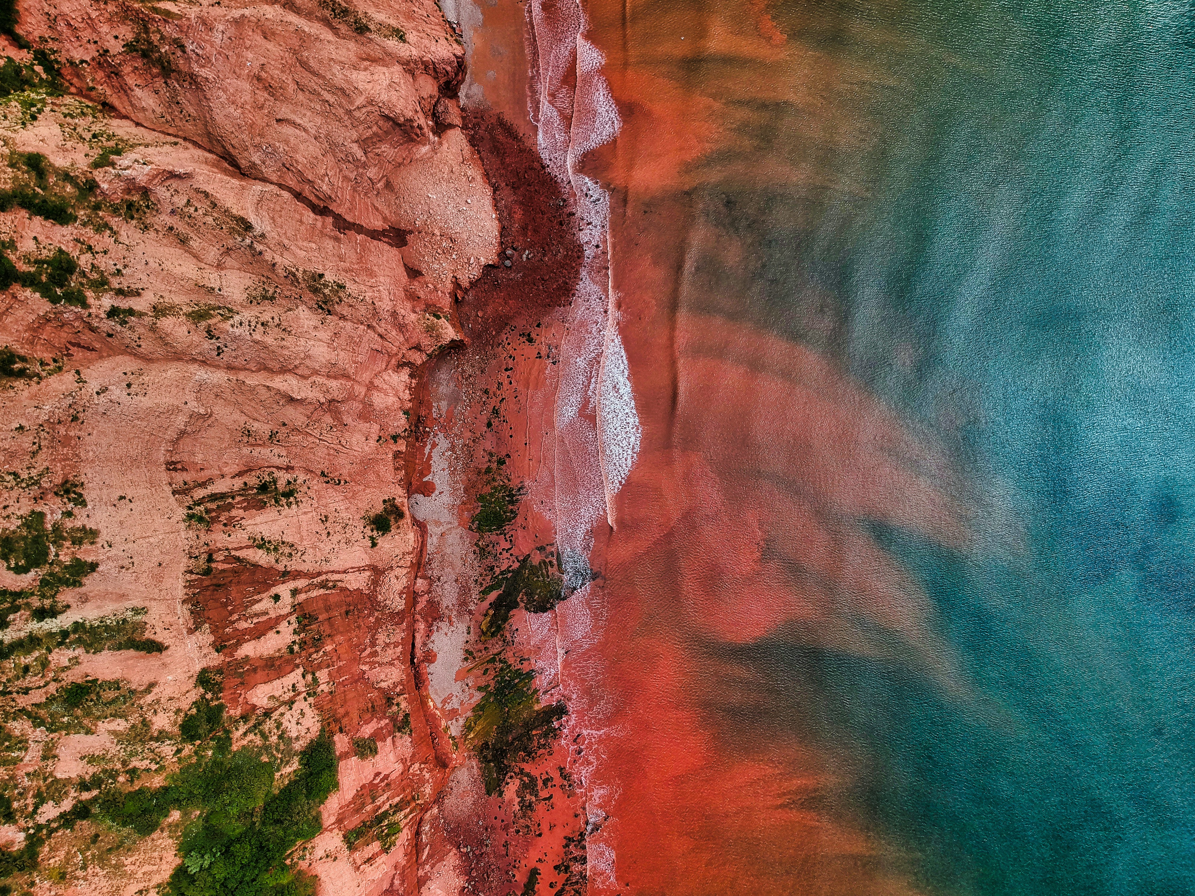 Aerial view of vibrant red cliffs meeting turquoise ocean waters.