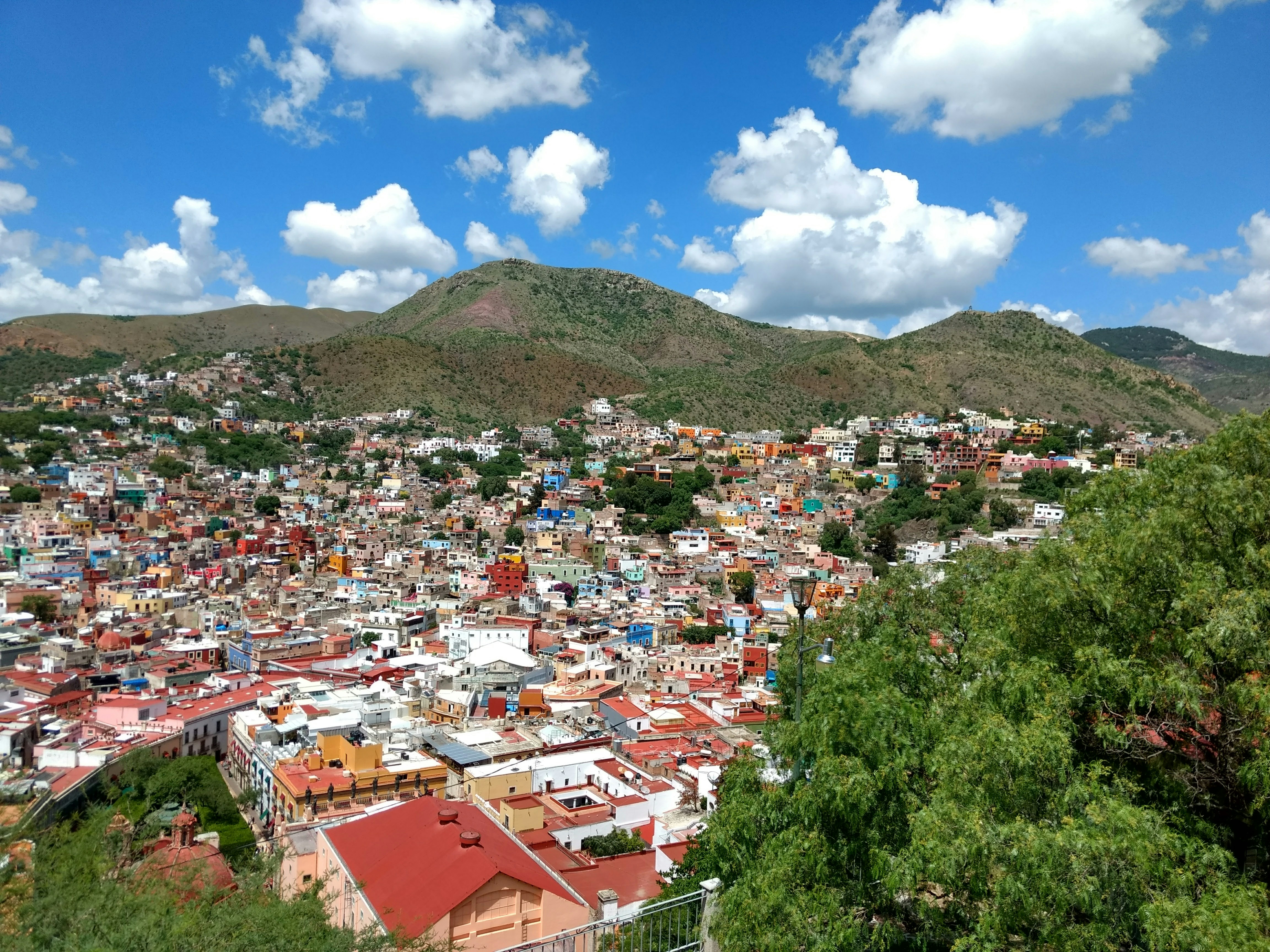 Vibrant cityscape of Guanajuato showcasing a patchwork of colorful buildings nestled among lush hills under a bright blue sky.