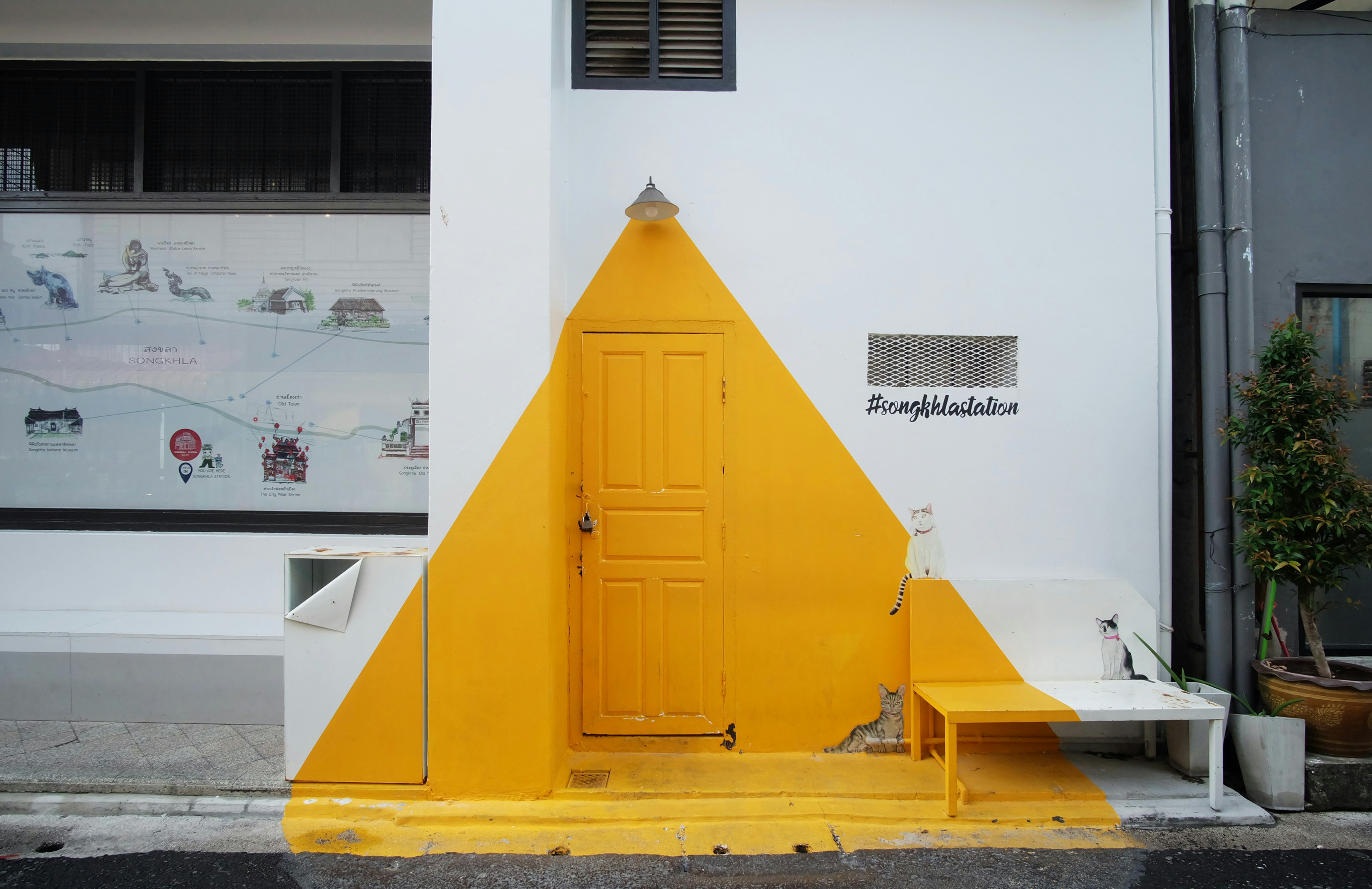 Vibrant yellow door integrated into a geometric mural on a white wall, complemented by minimalist furniture. A playful blend of art and architecture.