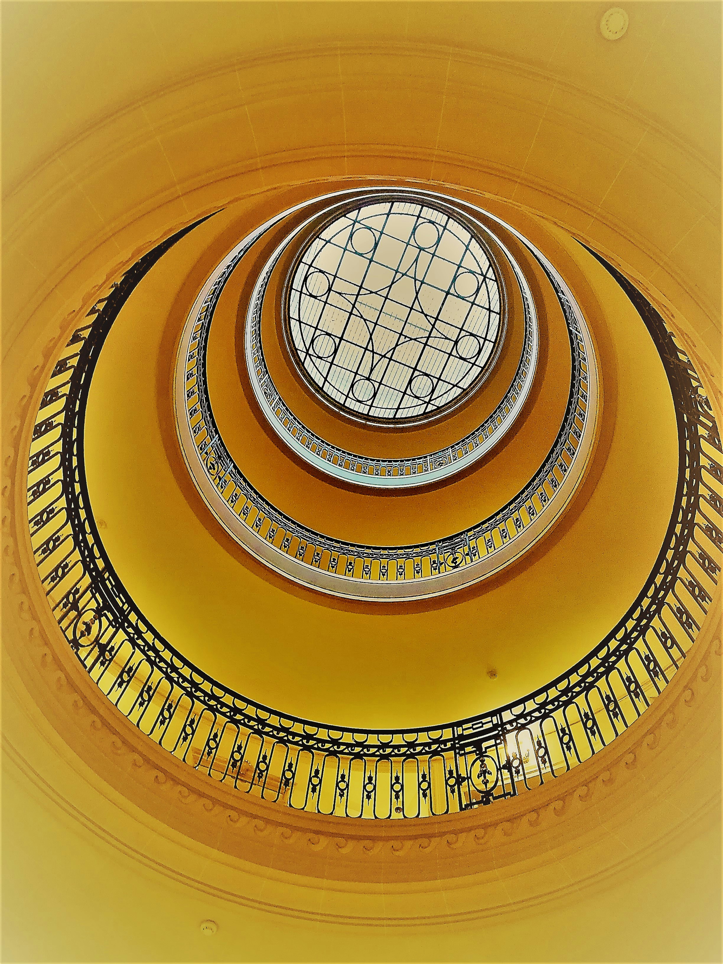 Intricate spiral staircase leading to a circular skylight, showcasing elegant architectural design and warm hues.