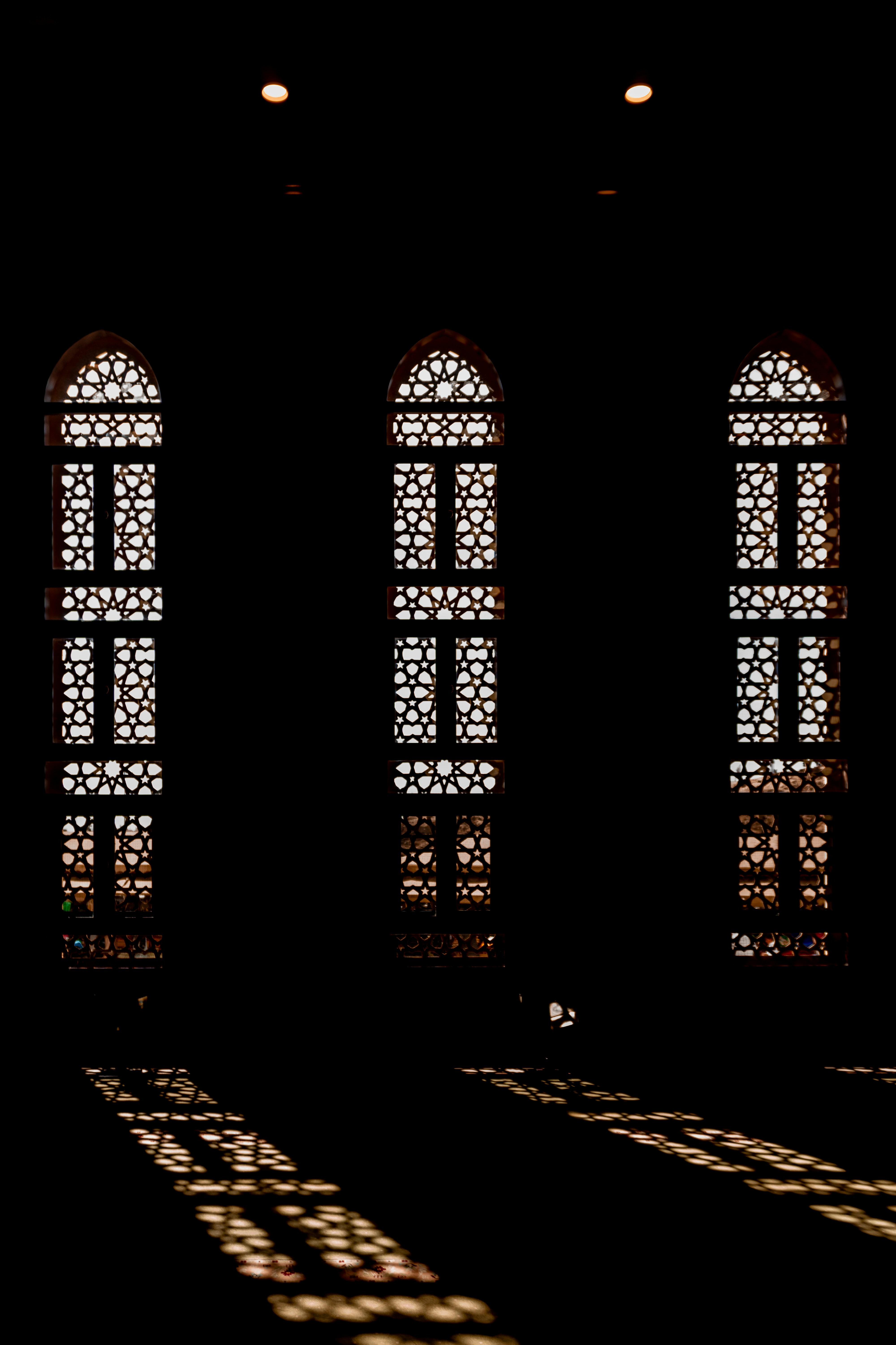 Intricate lattice windows casting geometric patterns on a dark floor, illuminated by soft light. The interplay of shadow and light creates a serene atmosphere.