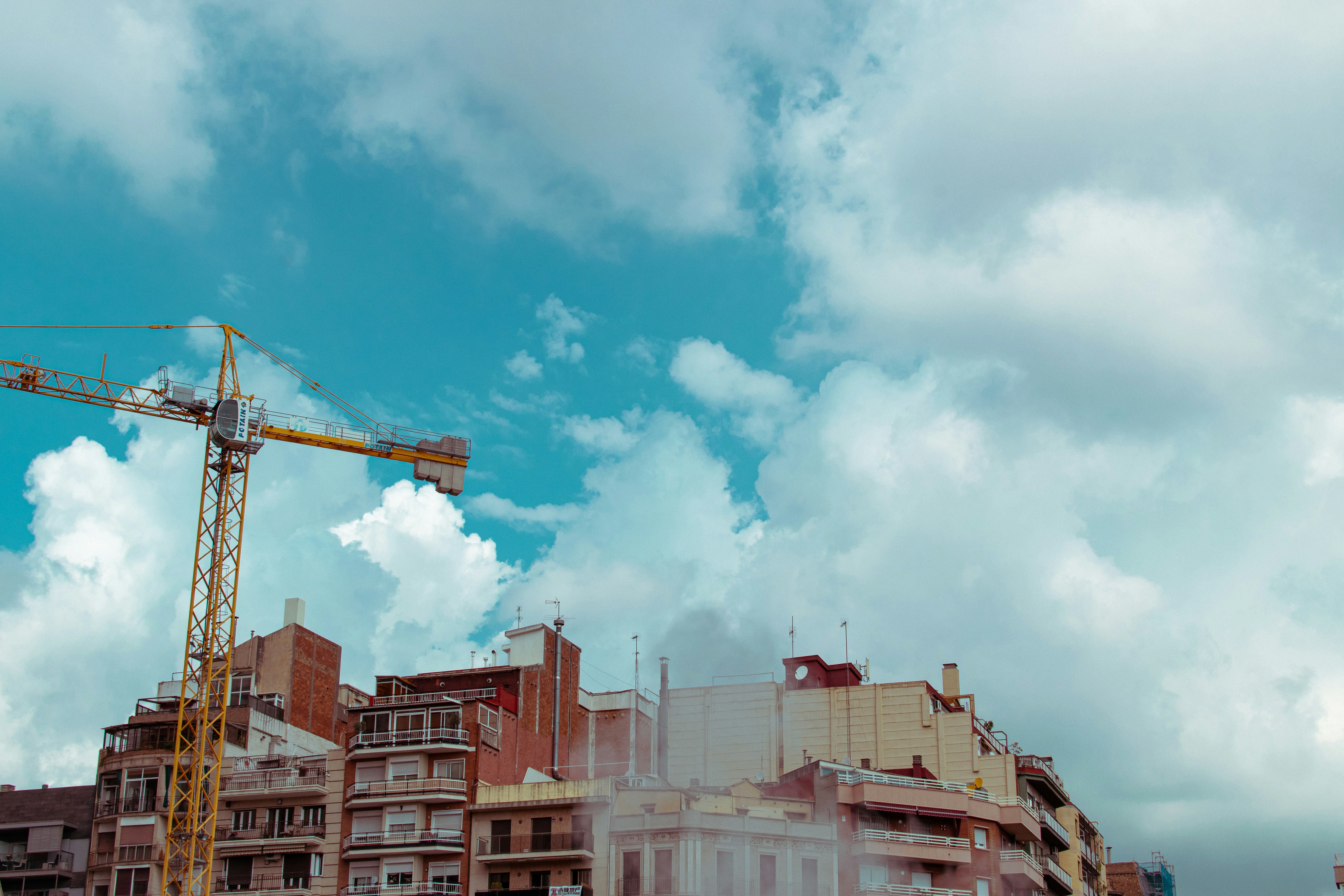 Construction crane towering over a cityscape, framed by vibrant clouds and blue sky. The scene captures the essence of urban development.