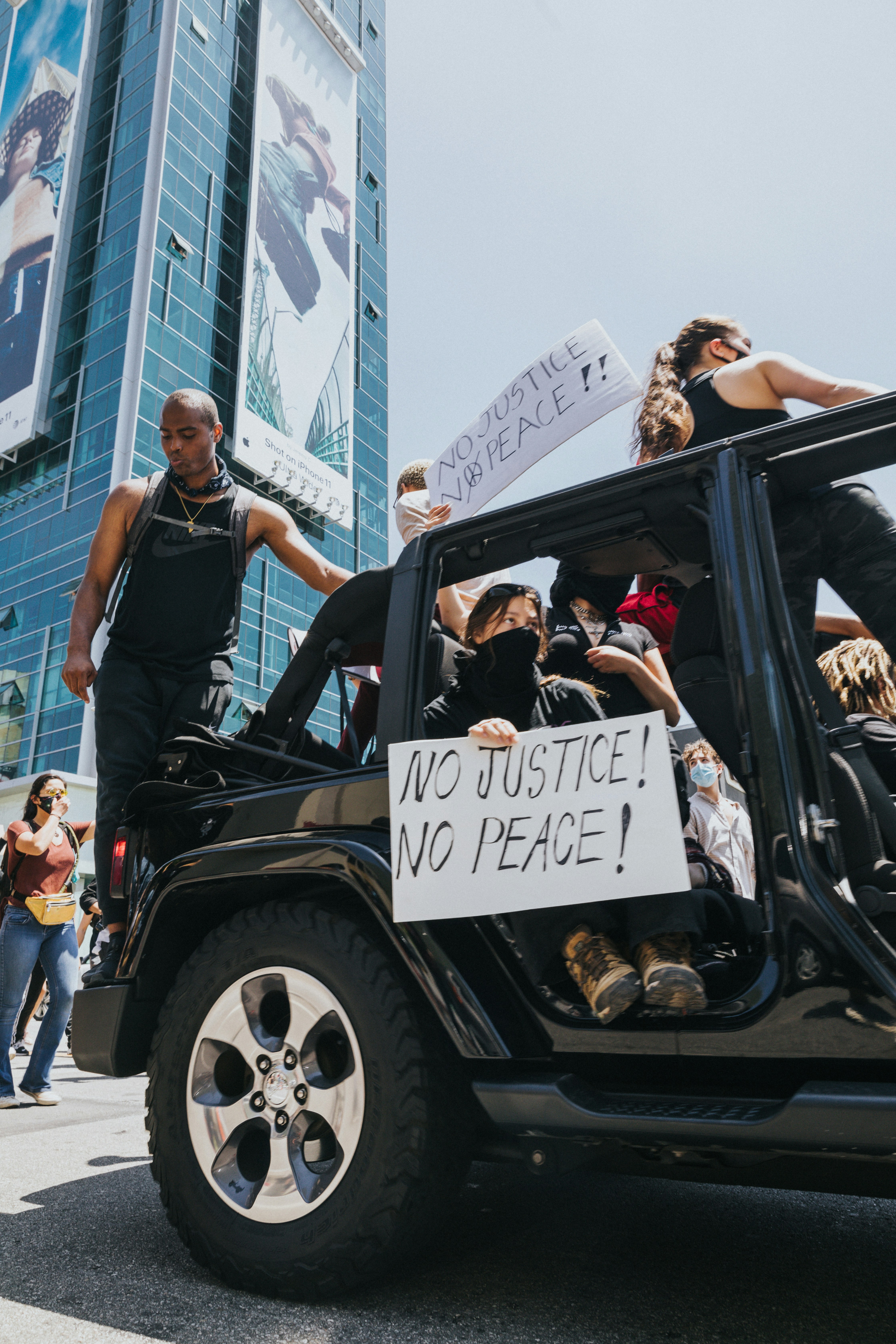 No Justice, No Peace: Protesters Crowding a Black Jeep Against a Glass-Fronted Cityscape