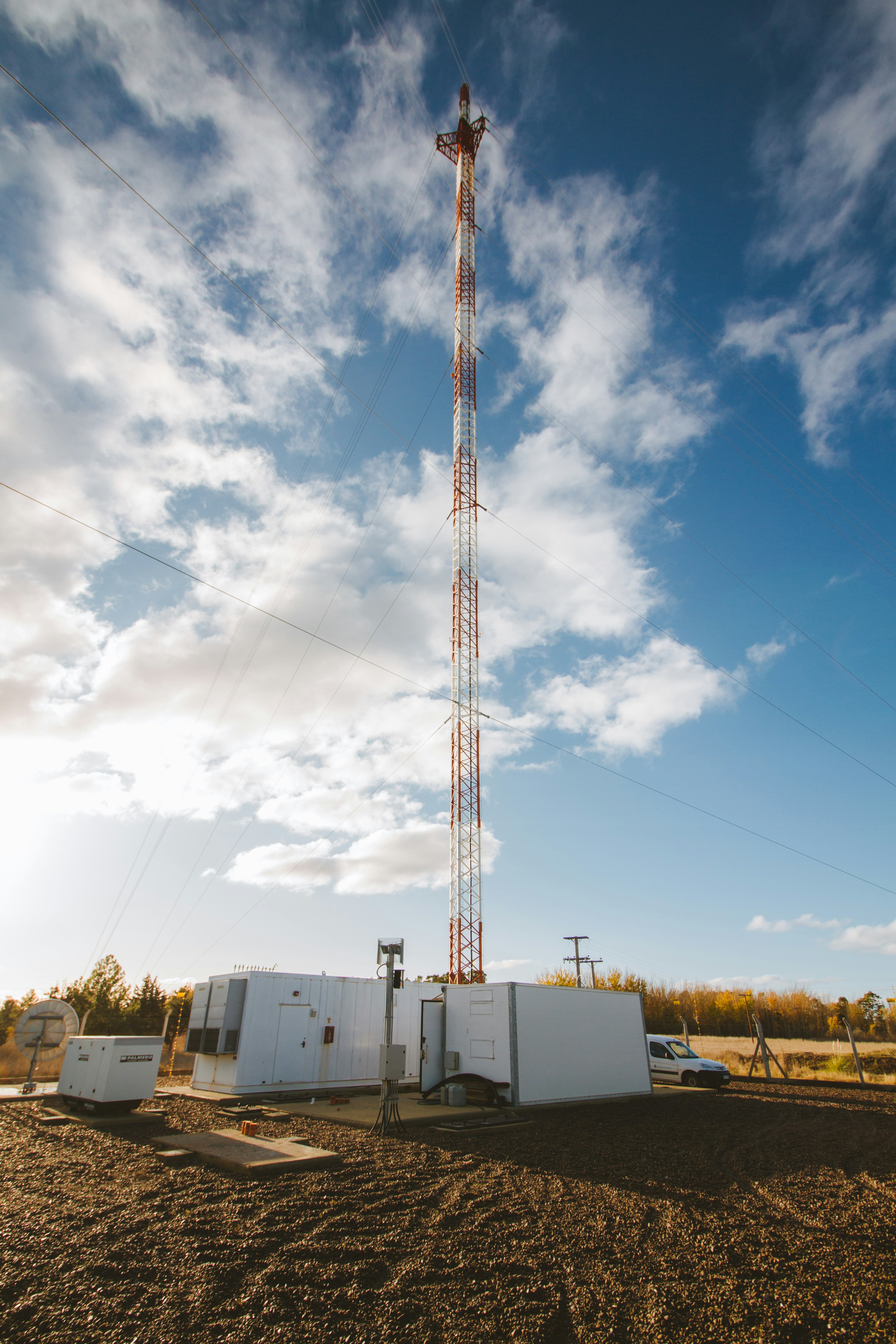 Tall communication tower under a vast sky with scattered clouds and sunlight illuminating the surrounding landscape.