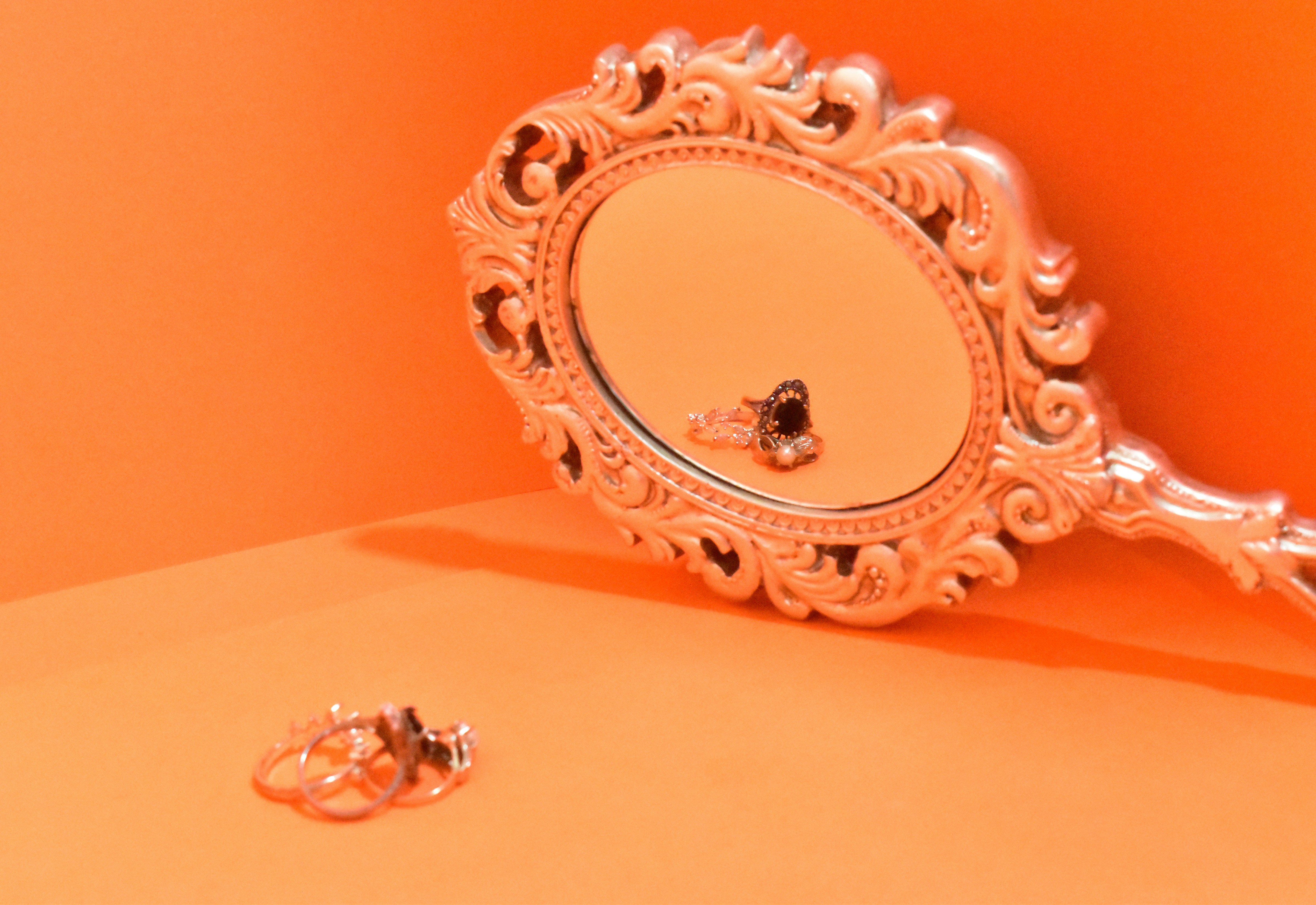 Amber Framed Glint: An Ornate Mirror and Ring in Tangerine Light
