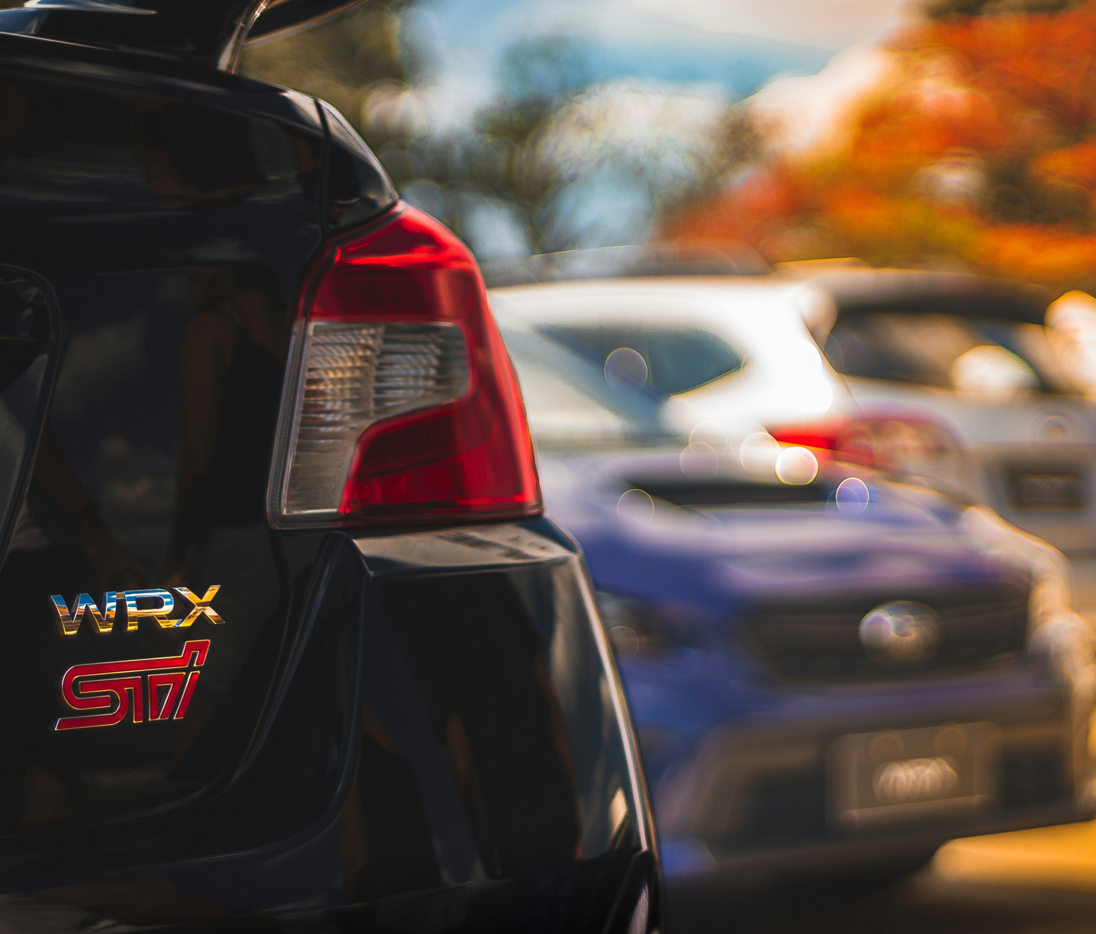 Close-up of a black Subaru WRX STI emblem with blurred cars in the background, showcasing automotive heritage and design.