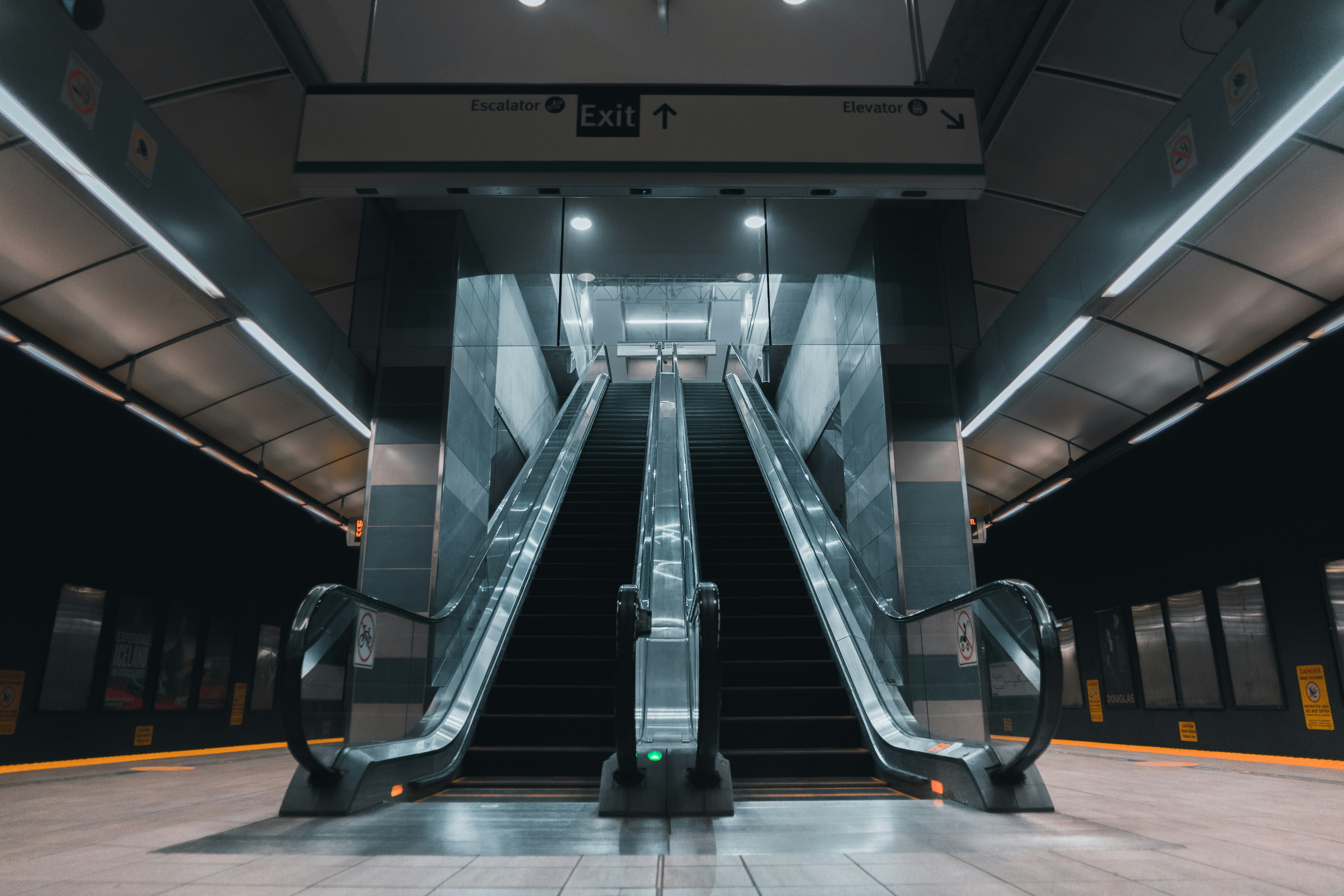 Modern escalators in a dimly lit subway station with sleek metallic surfaces and glowing lights.