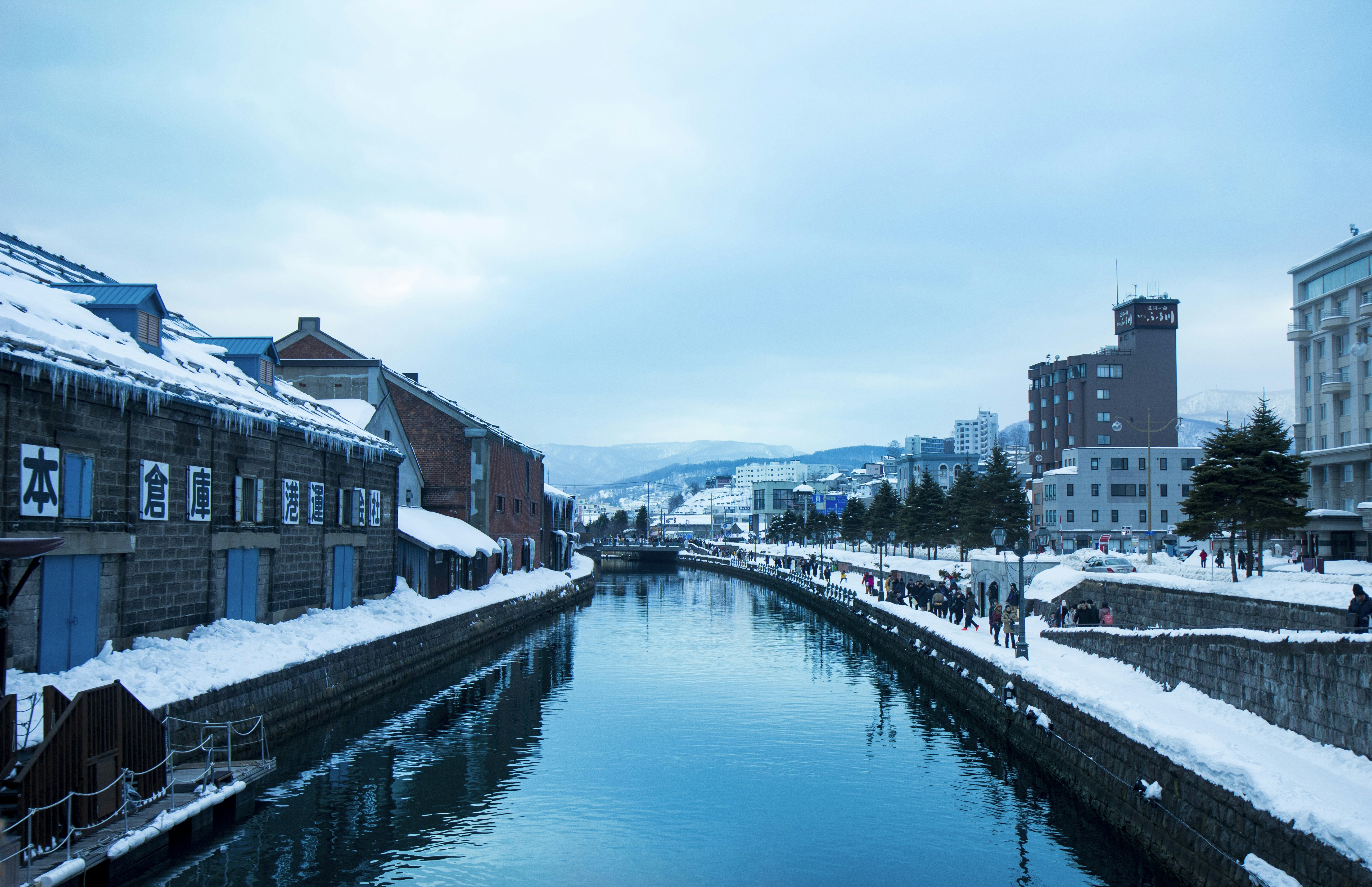 Snow-covered buildings line a tranquil canal under a cloudy winter sky.