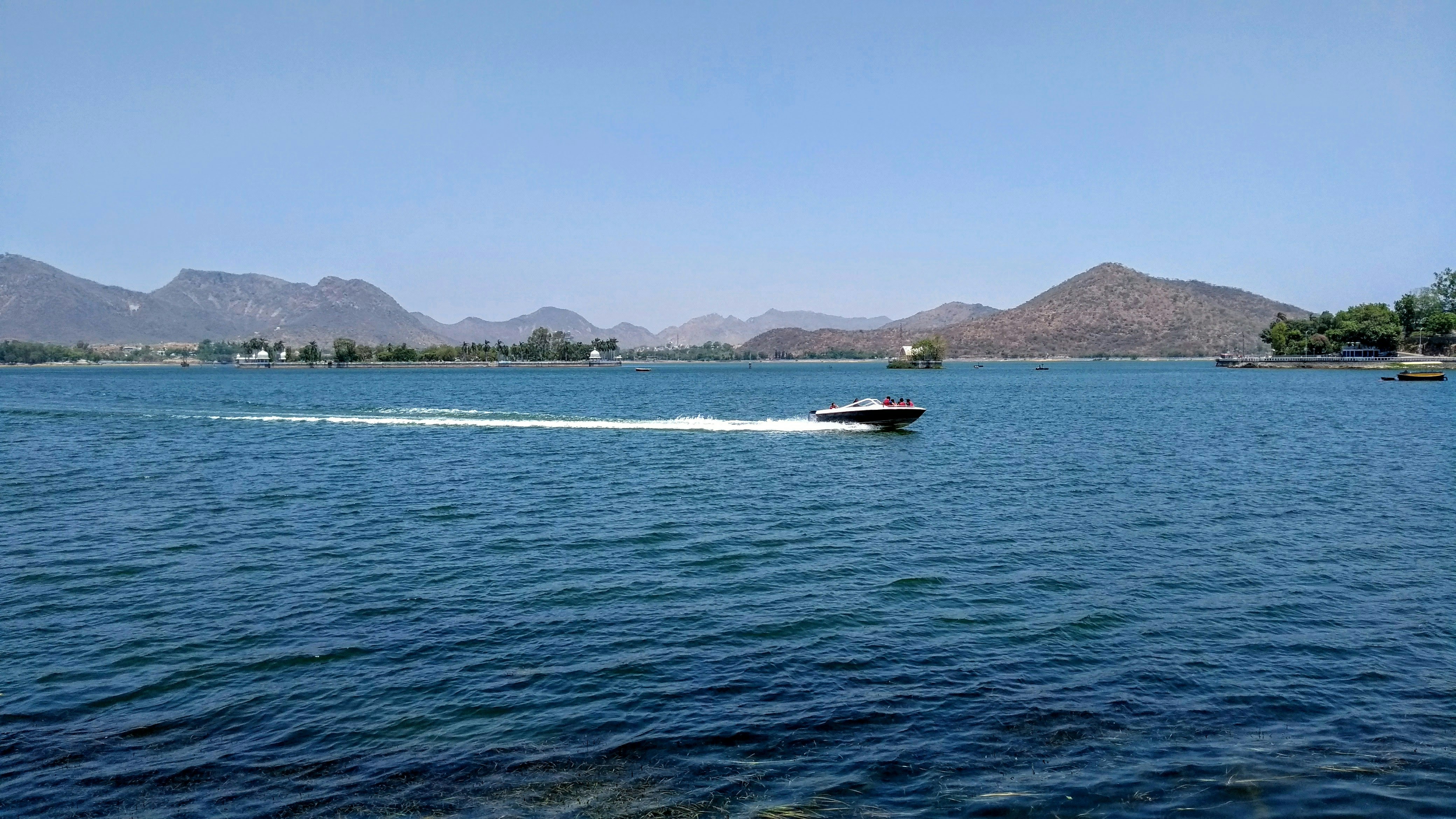 Speedboat slicing through the calm blue waters of Fateh Sagar Lake with distant mountains under a clear sky.